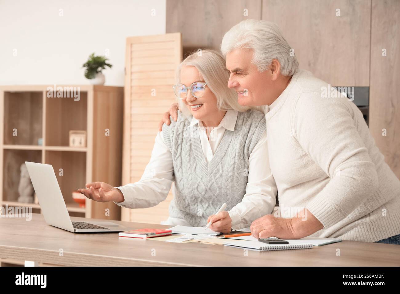 Senior couple with laptop calculating utility bills at table in kitchen ...