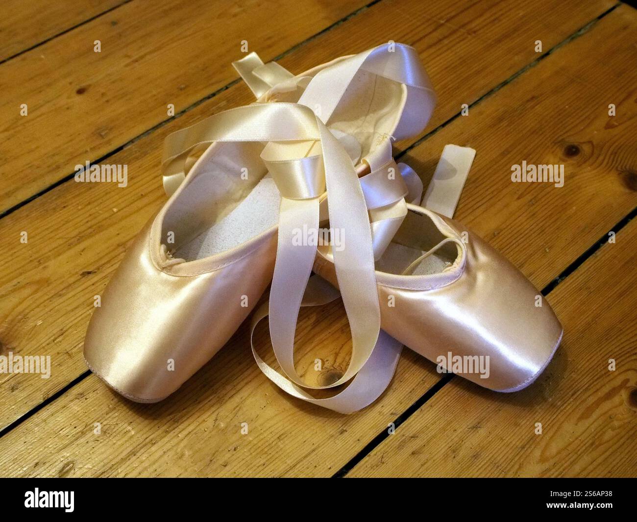 A pair of pointe shoes on a wooden floor with the ribbons, which tie ...