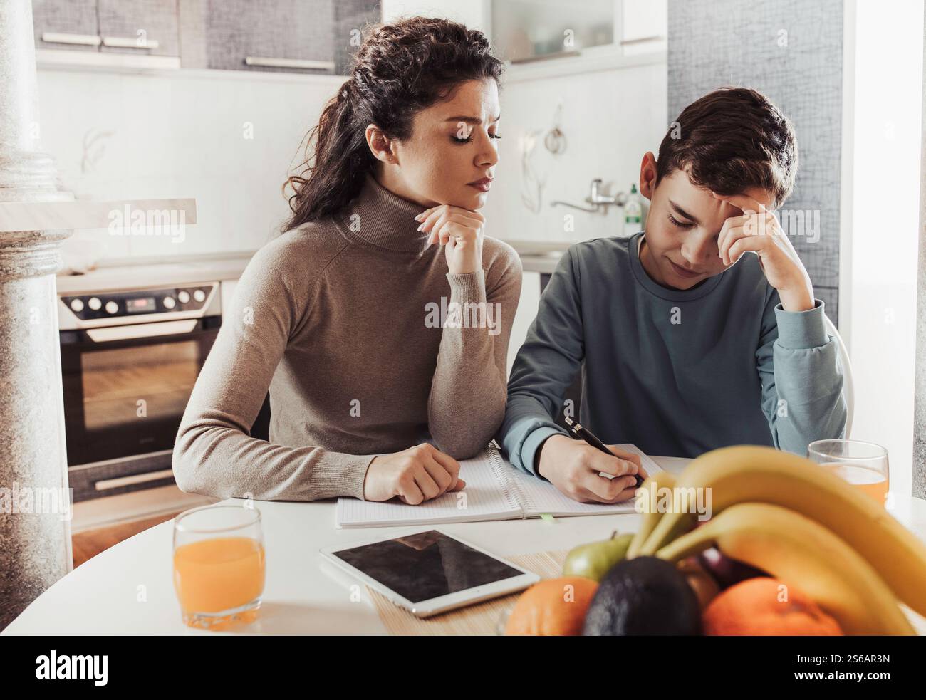Strict mother checking how son doing homework at dining table at home ...