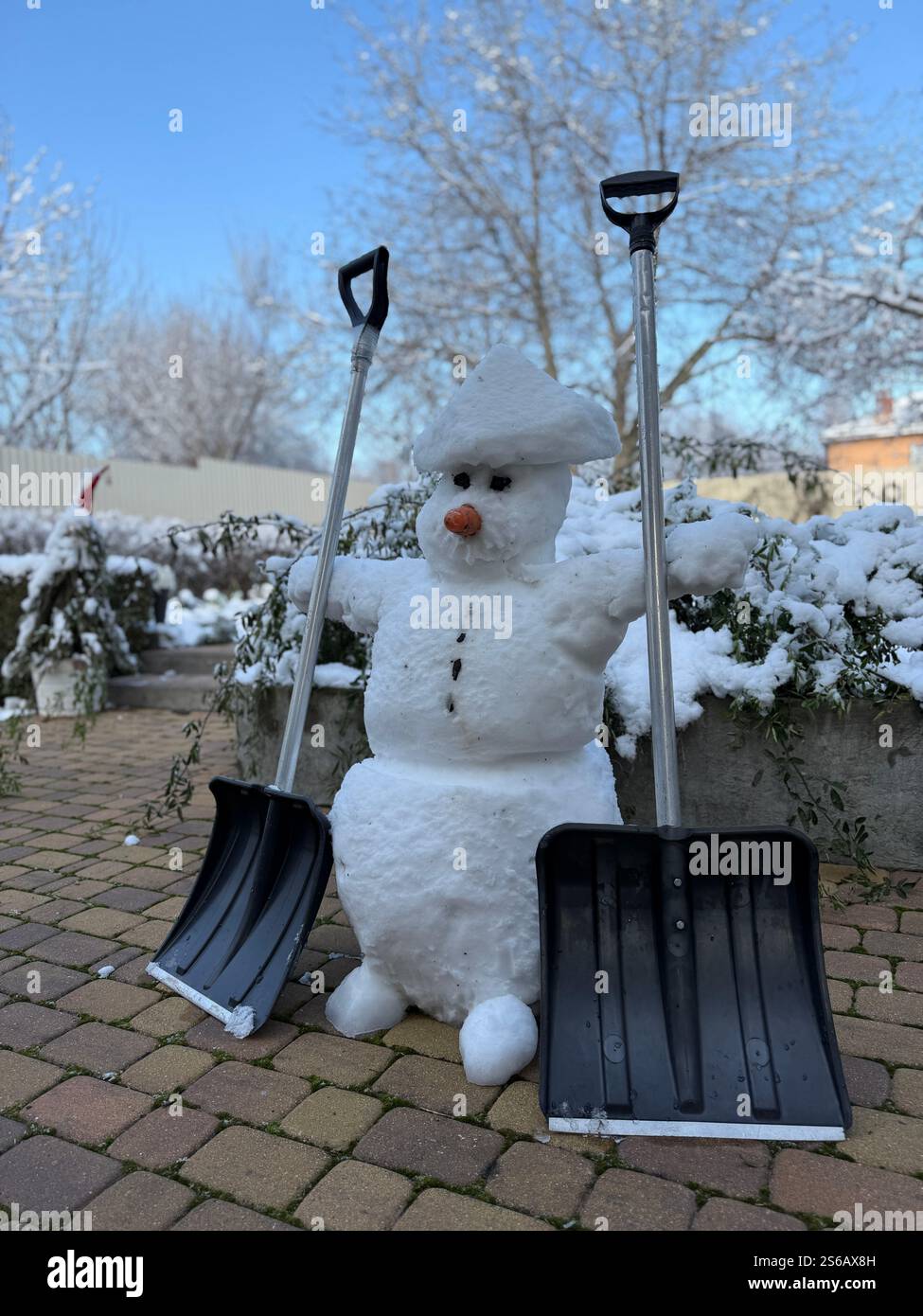 funny snowman holding shovels in his hands, made of snow in the yard of ...