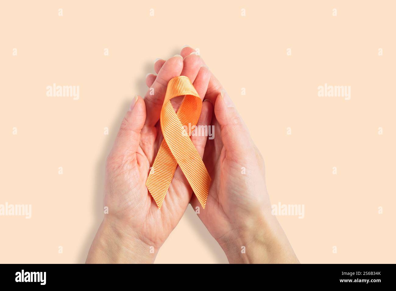 Orange cancer awareness ribbon in womens hands on white background ...