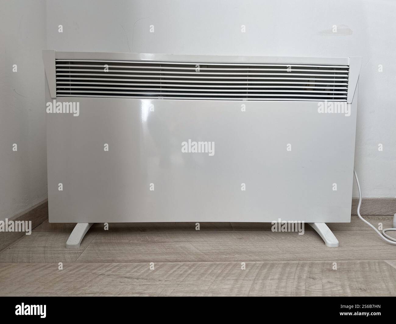 Modern white electric heater placed against a plain wall. Functional ...