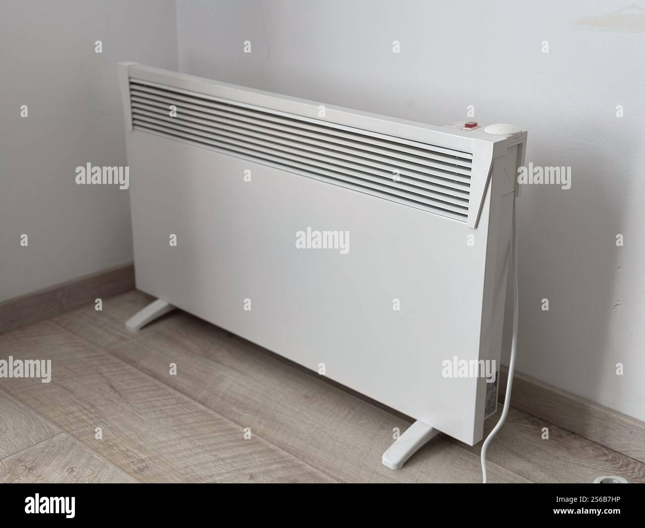Modern white electric heater placed against a plain wall. Functional ...