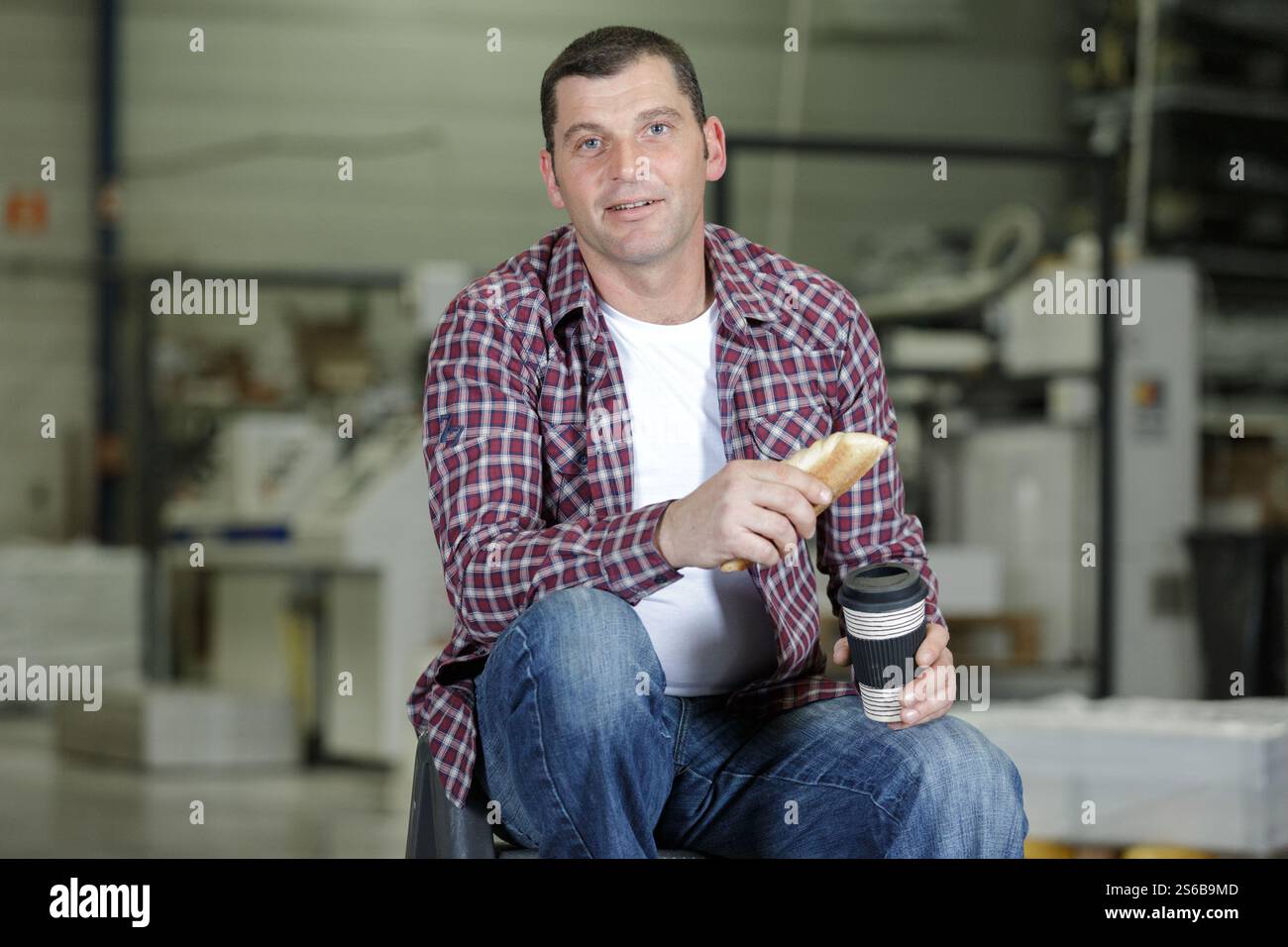 portrait of cheerful factory worker eating sandwich during lunch break ...