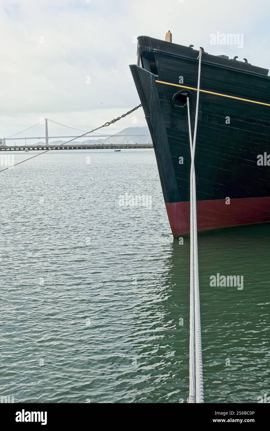 Mooring lines lead to bow of 19th century sailing ship with distant ...