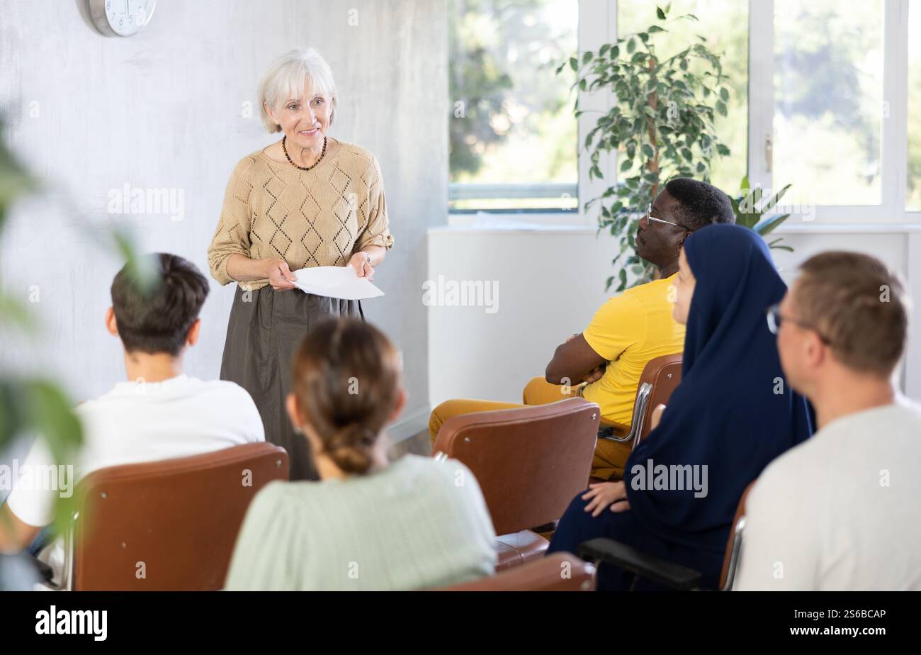 Elderly woman giving lecture to international adult group Stock Photo ...