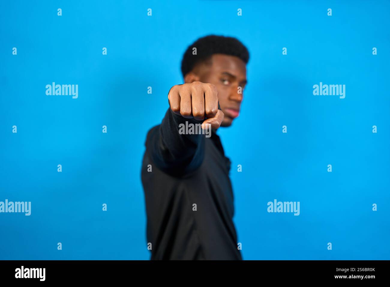 Serious young black man throwing a punch towards the camera against a ...