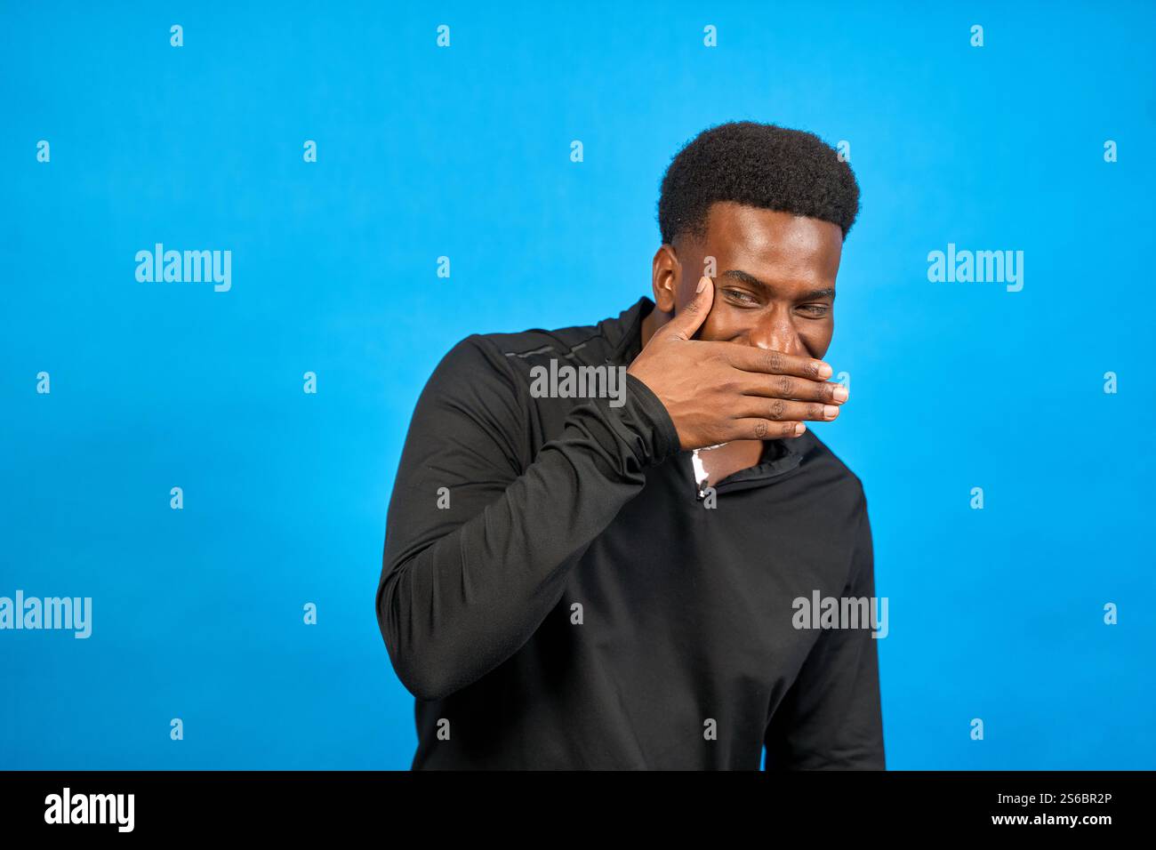 Studio portrait of a young man covering his mouth with his hand while ...