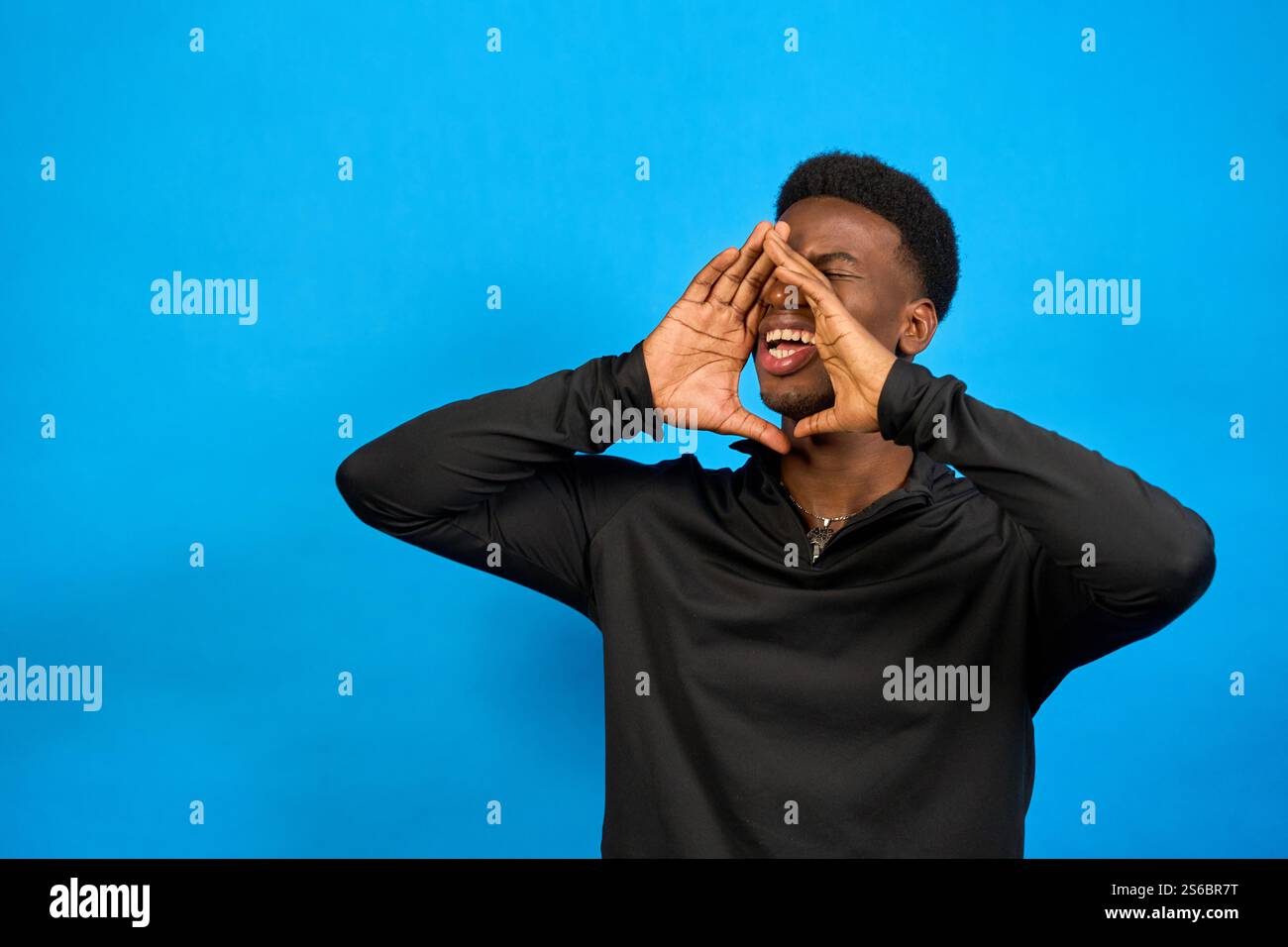 Cheerful young adult male shouting with hands cupped around mouth ...