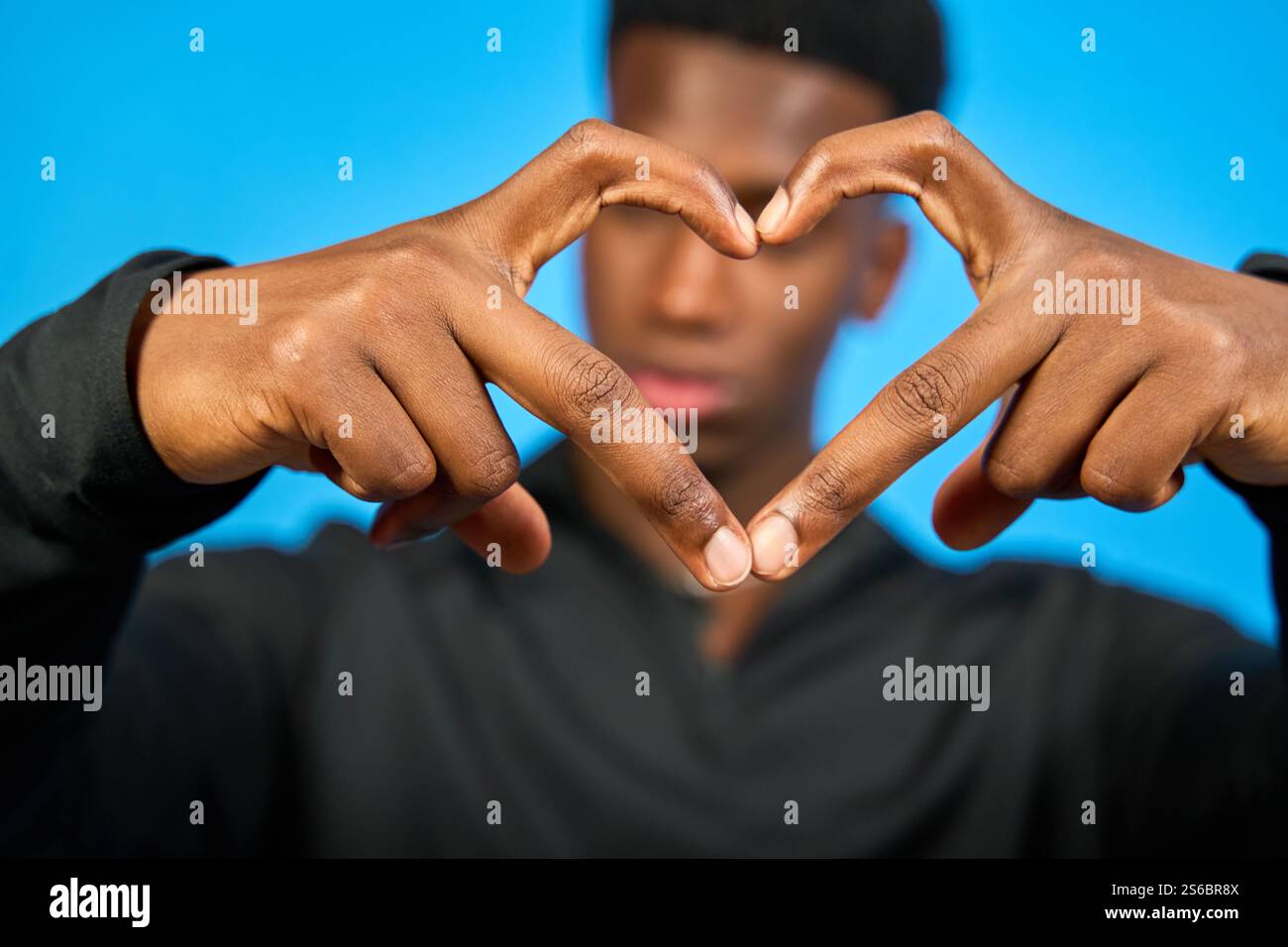 Young man making heart shape with hands on vibrant blue background ...