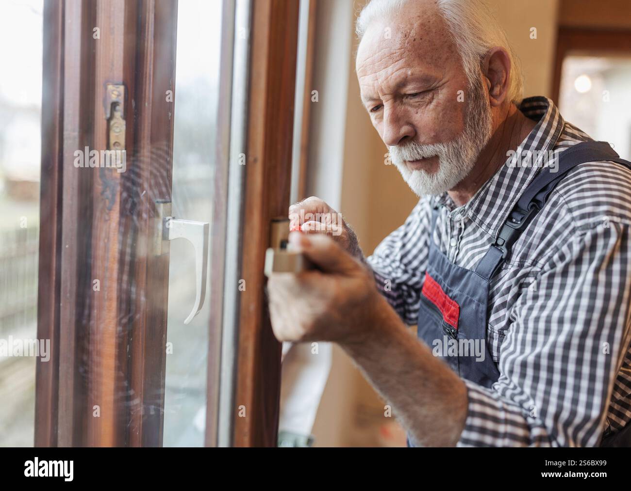 Portrait of mature craftsman fixing window handle inside house Stock ...