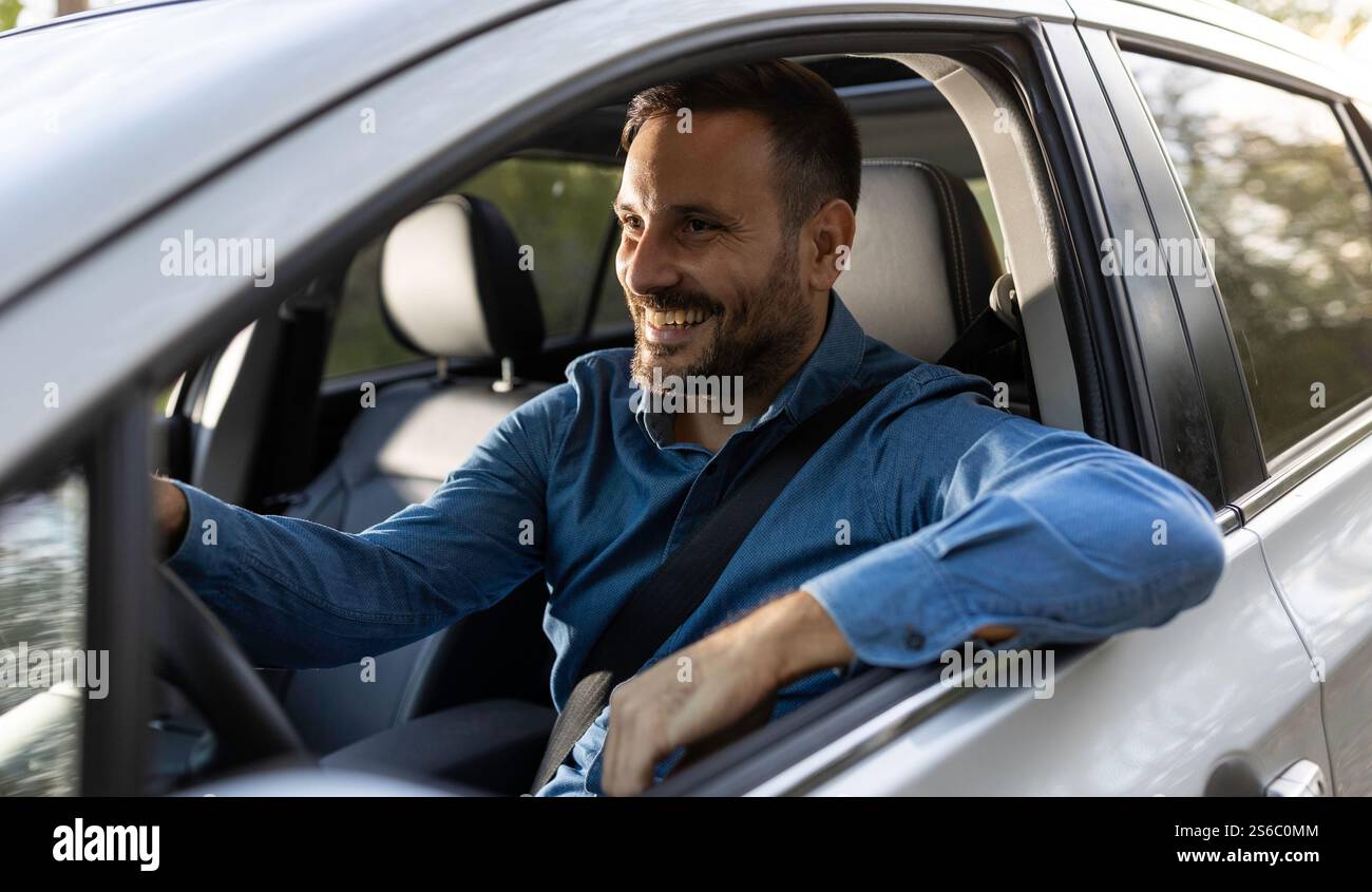 Cheerful man driving car with open side window and elbow outside on ...