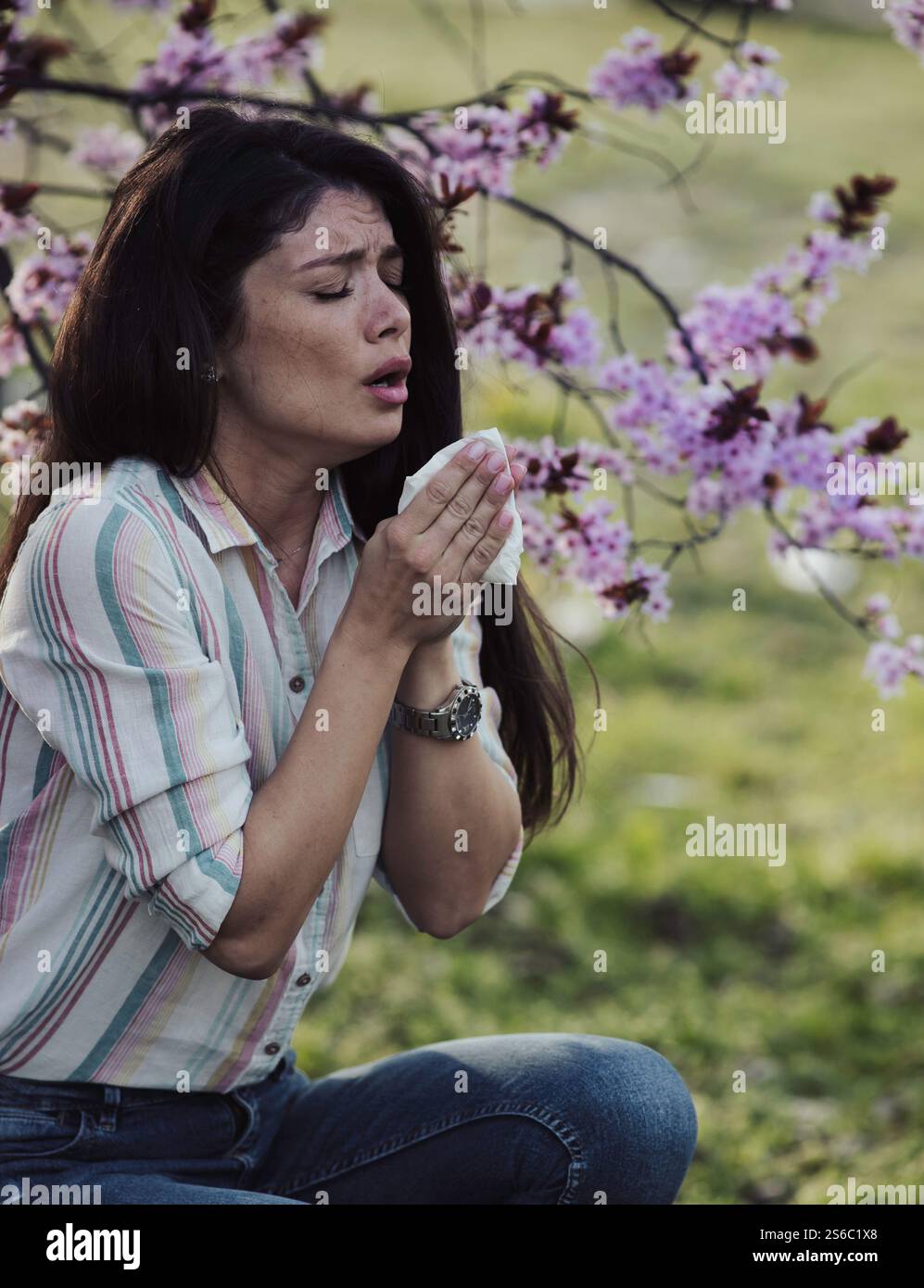 Young woman sneezing in napkin in front of blooming tree. Spring ...