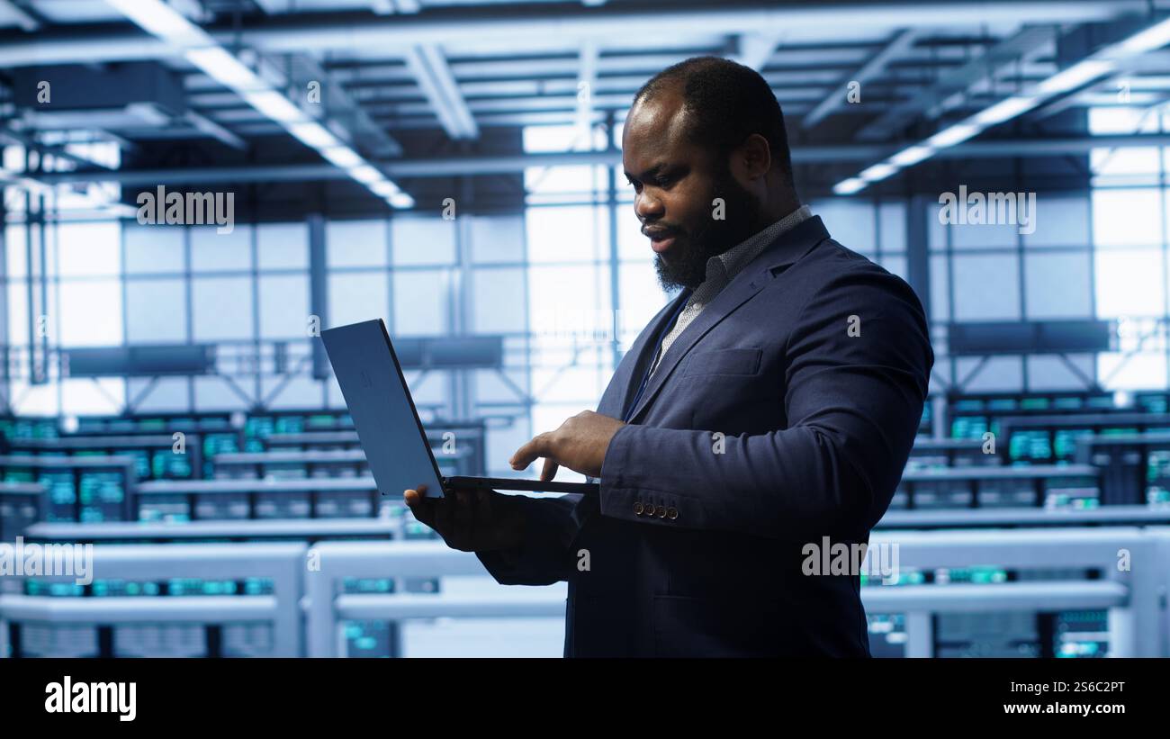 Computer scientist in server hub checking recovery plan on laptop, monitoring hardware energy ...