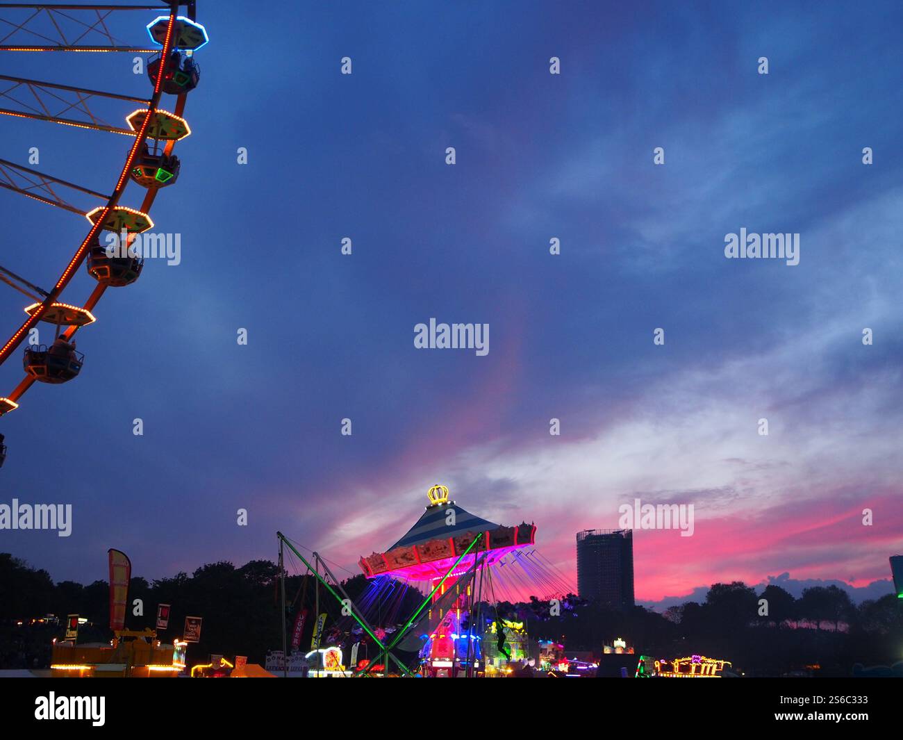 A lit-up carousel in front of the sunset behind the Post tower with a ...