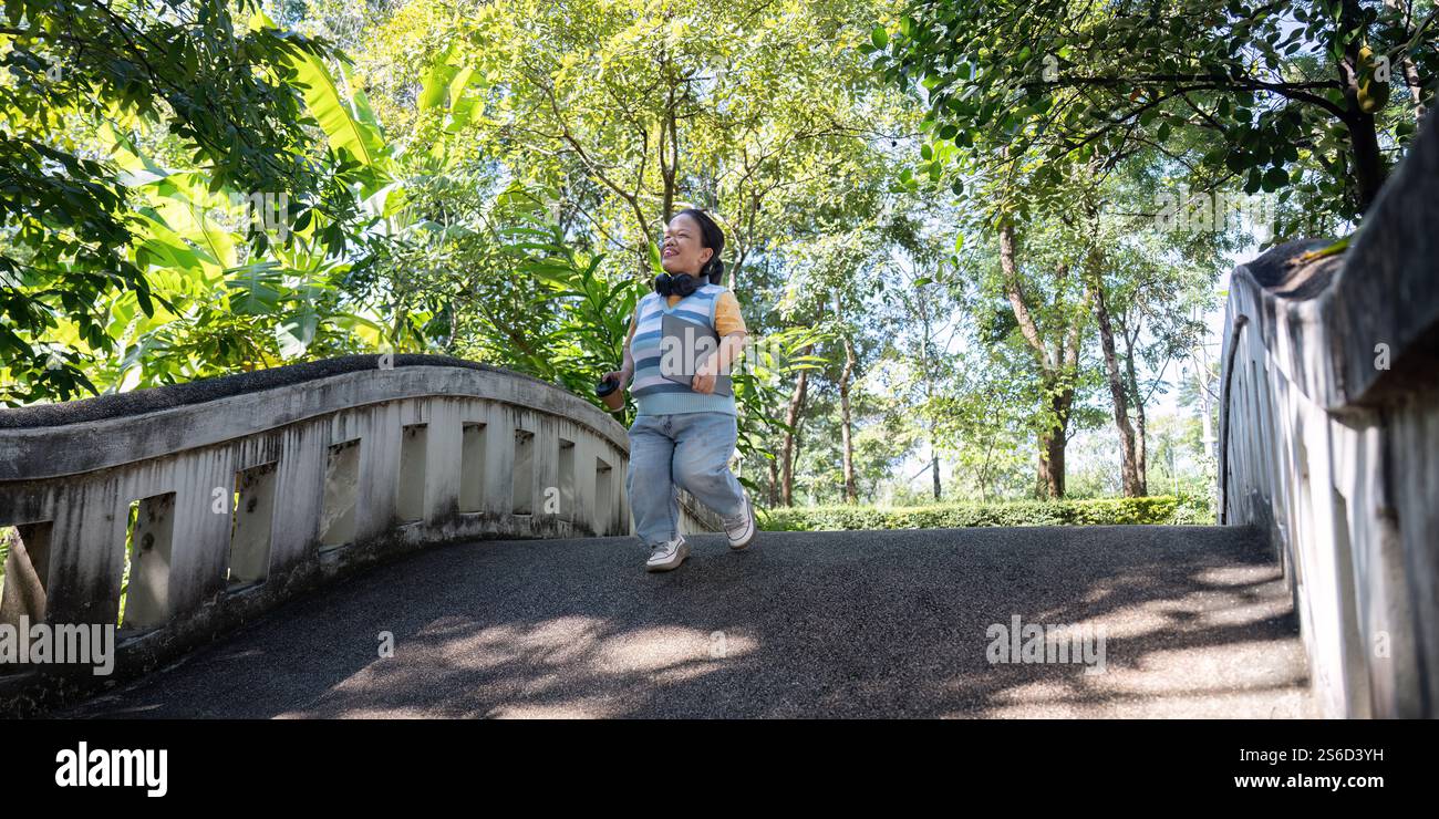 Joyful child with achondroplasia running on a bridge in a lush green ...