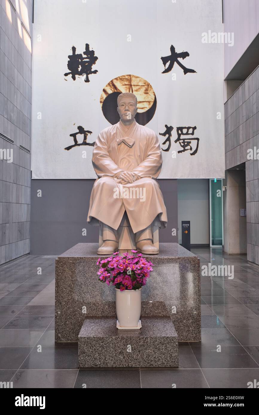 A large, white statue, sculpture of a sitting, somber Ahn Jung-geun ...