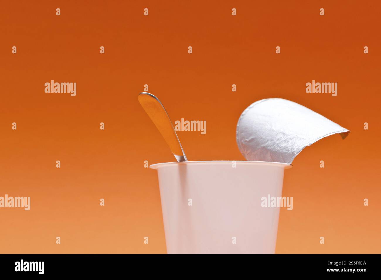 An empty clean yogurt cup with spoon on an orange background Stock ...