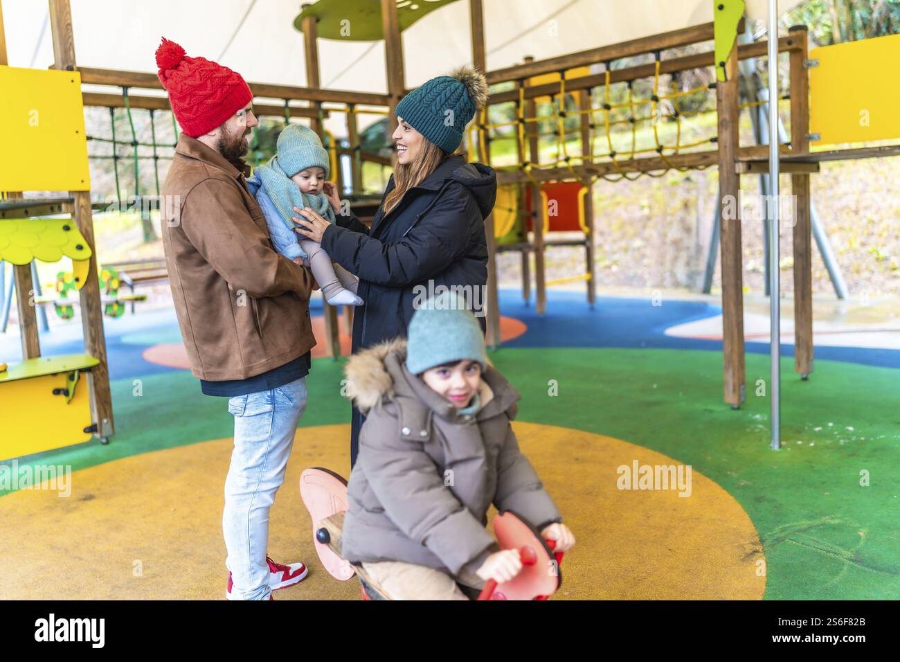 Family enjoying time together at the playground, with parents holding ...