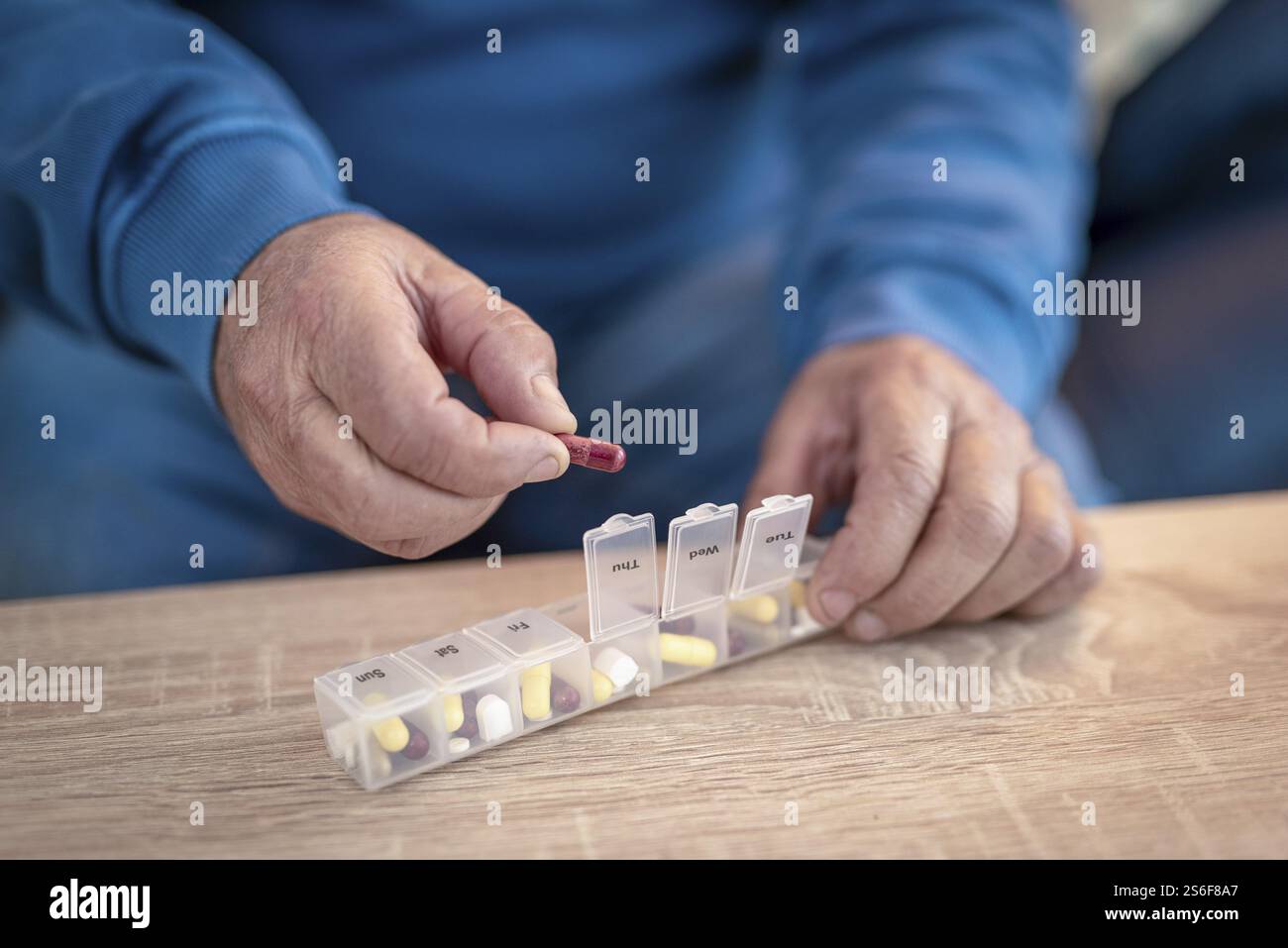 Elderly man picking a red pill from a weekly pill organizer, managing ...