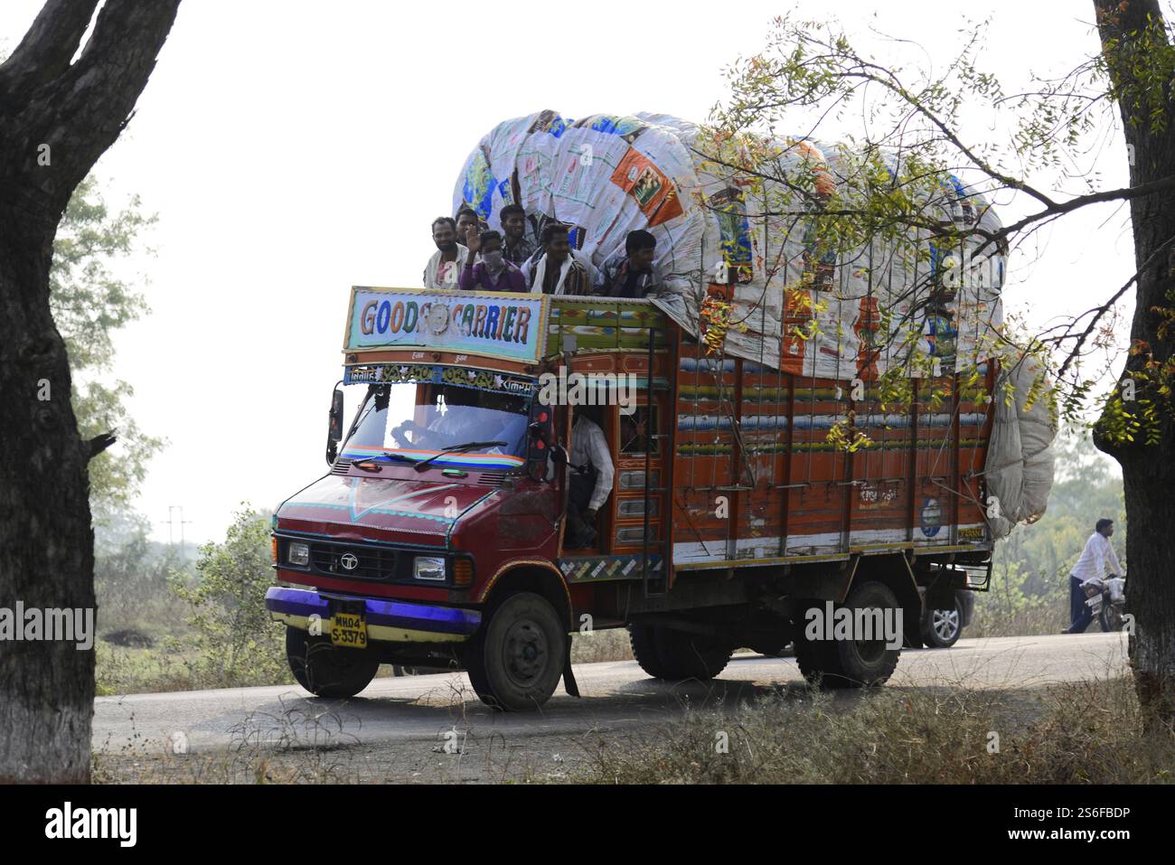 An overloaded lorry with people on the back is driving on a road ...