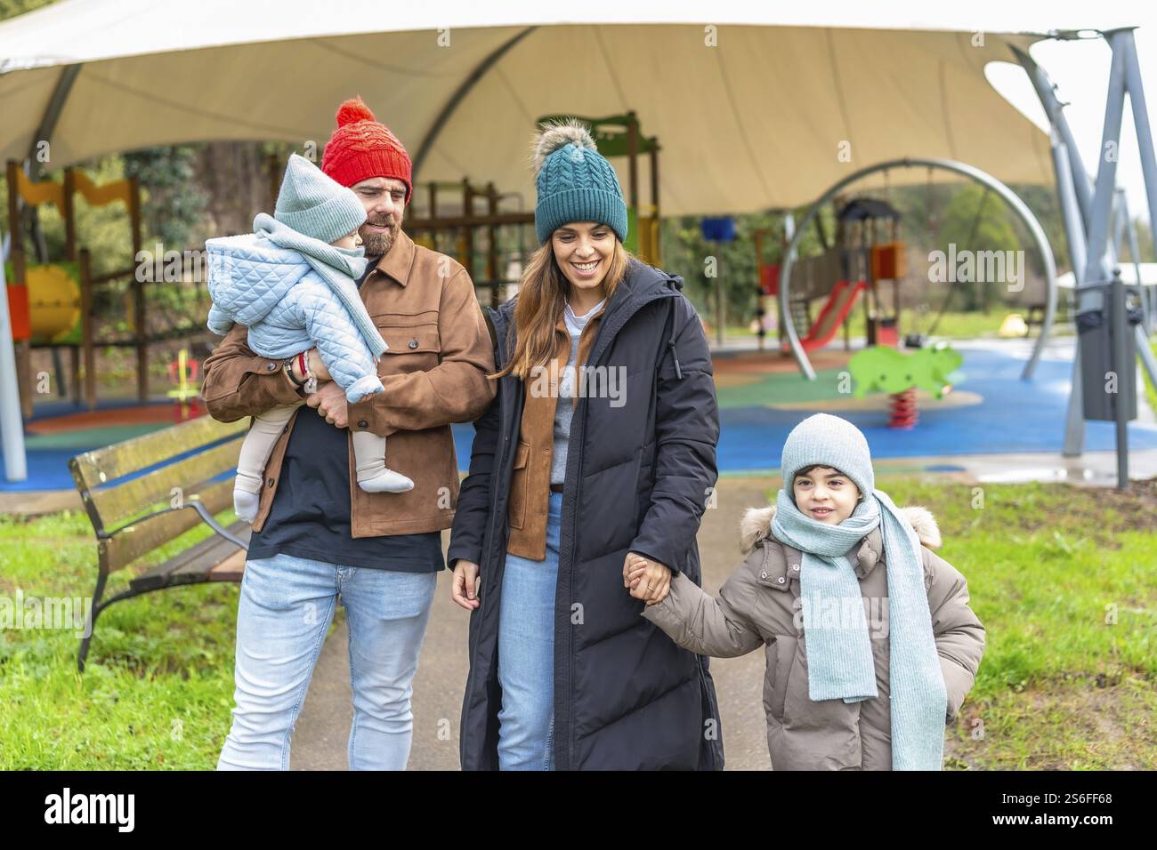 Smiling parents holding their children's hands are walking in a ...