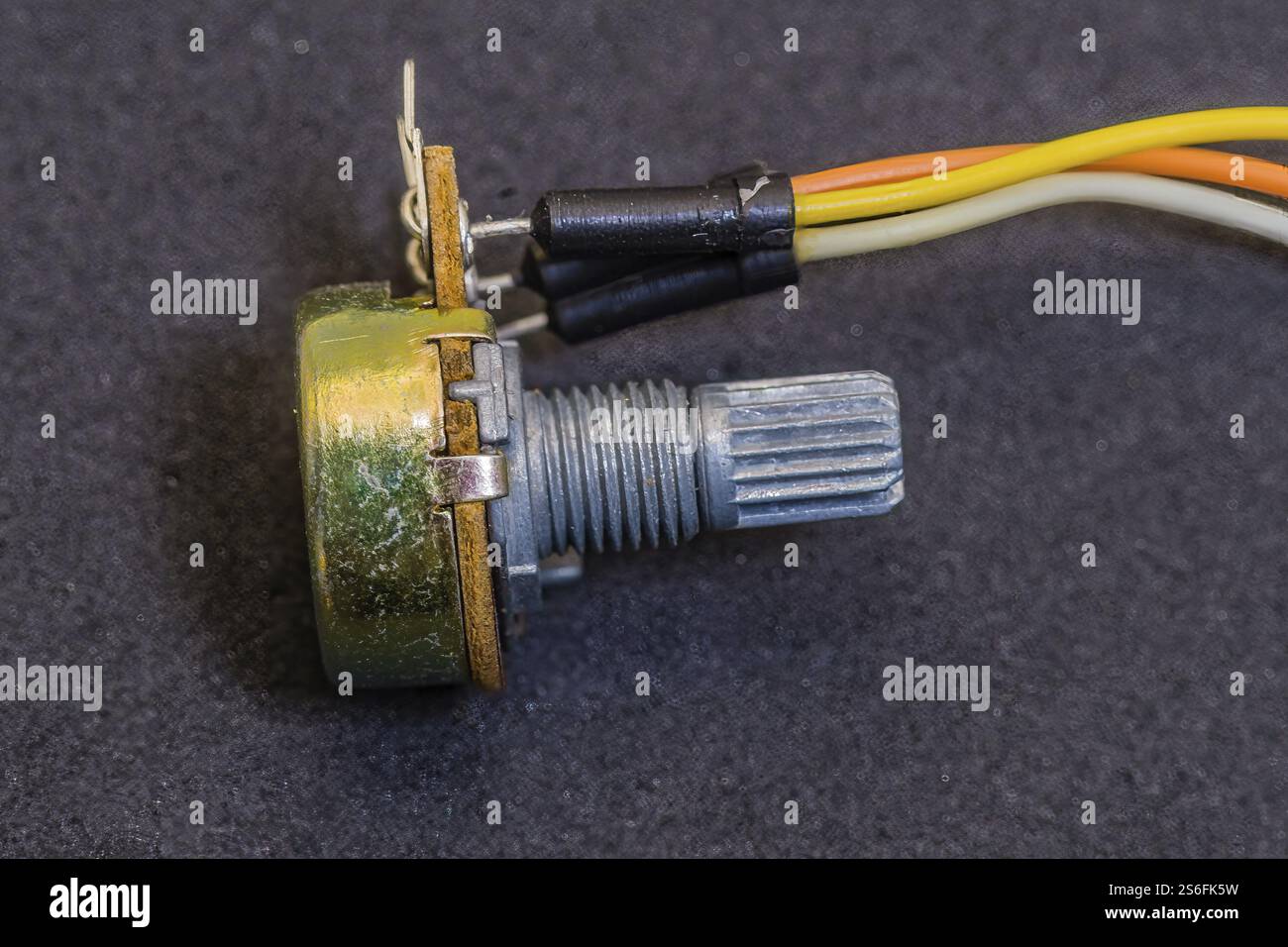 A metal potentiometer with wires attached, lying on a dark background ...