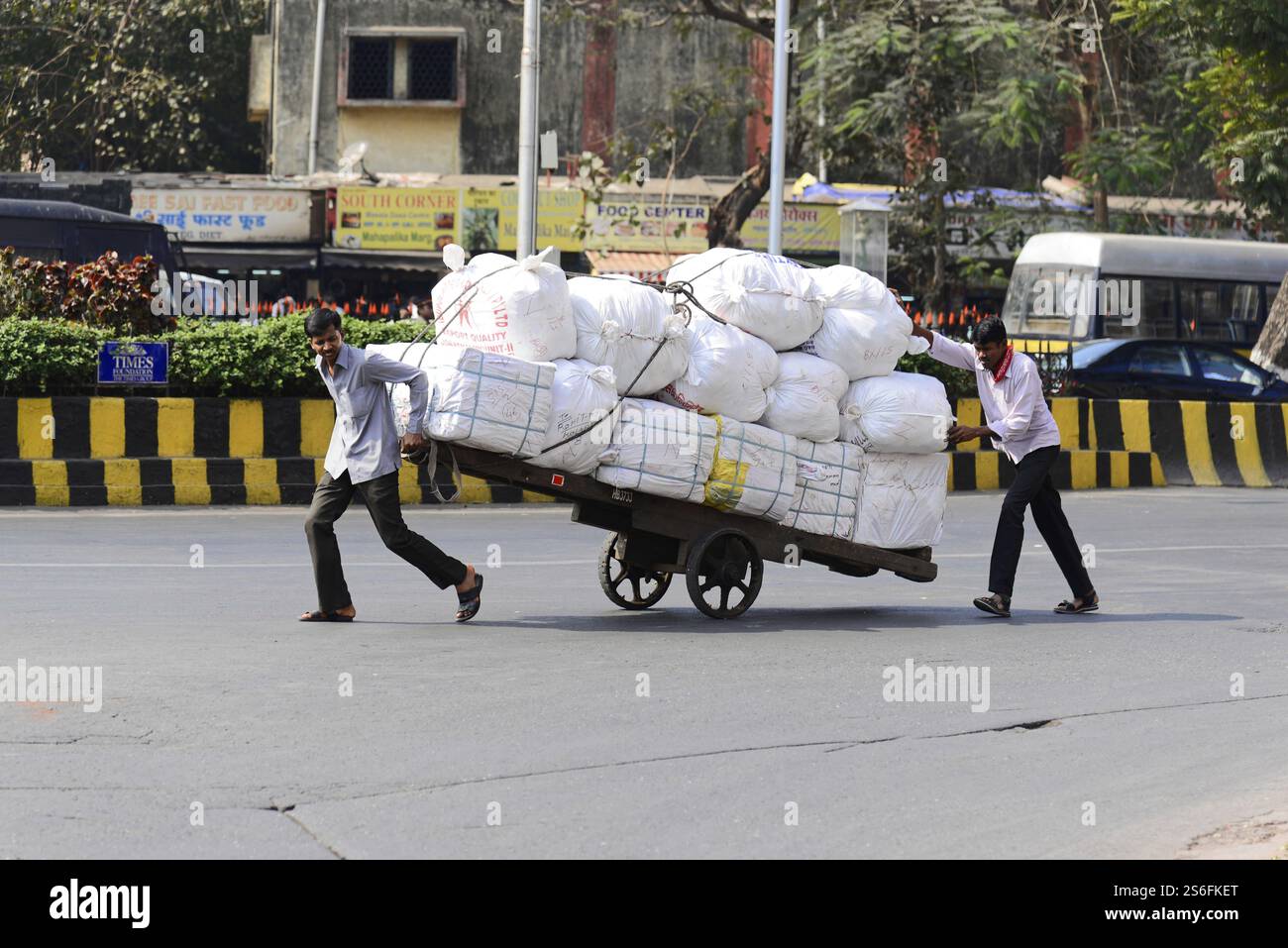 Two men transporting a full, heavily loaded cart across the road ...