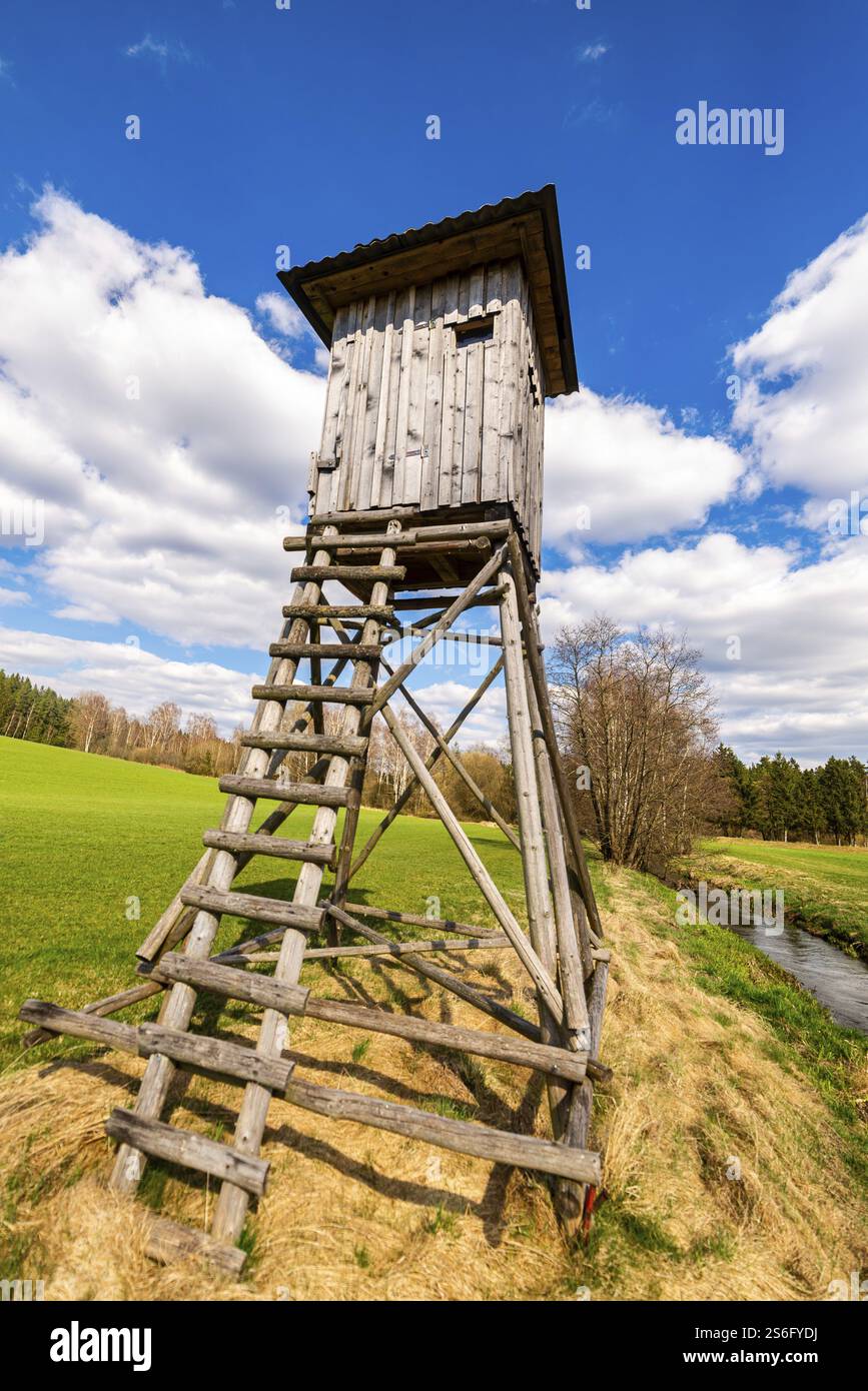 A hunting hide on the edge of a small stream under a blue sky with fair ...