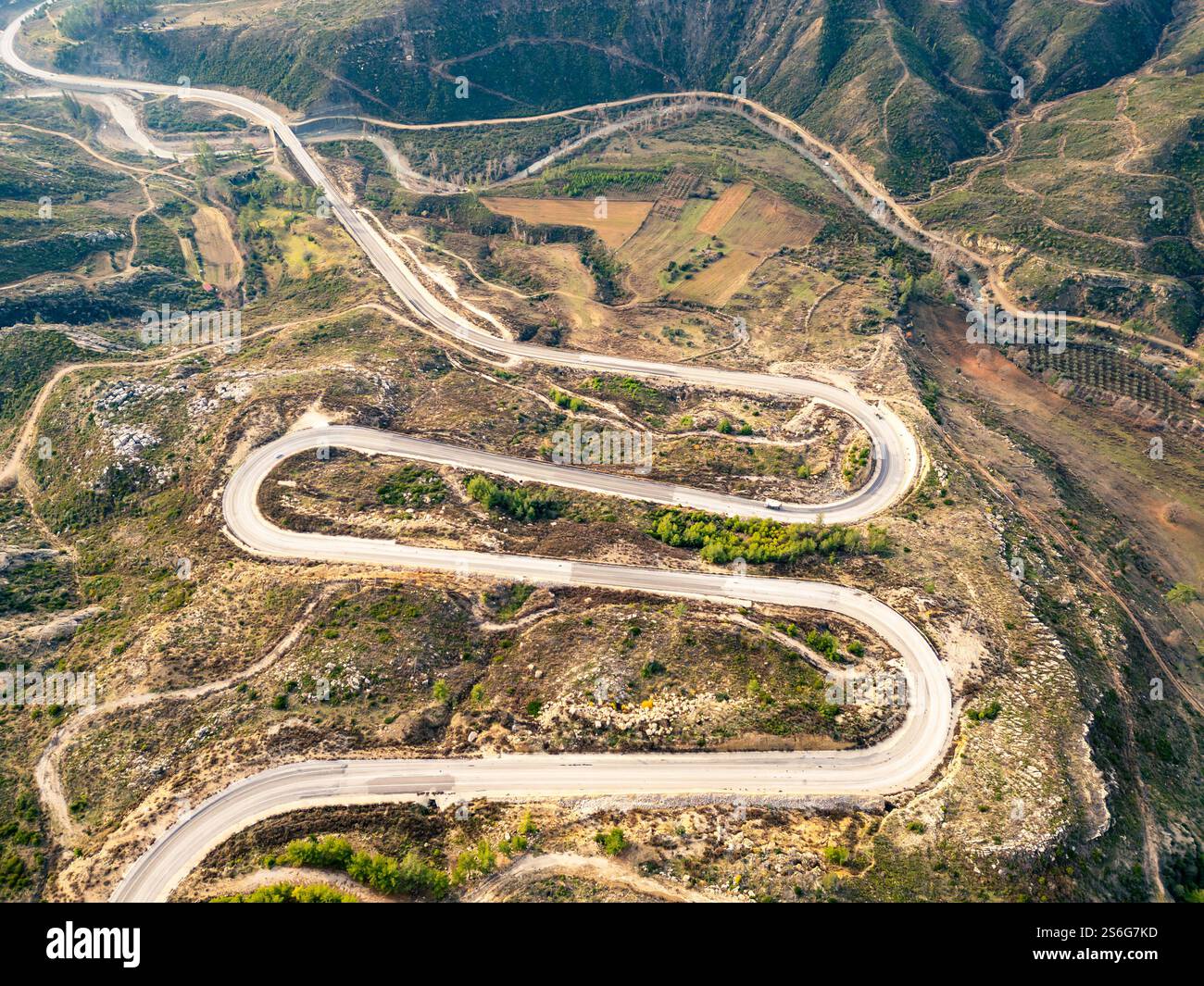 A winding asphalt road that passes through areas with few trees in ...