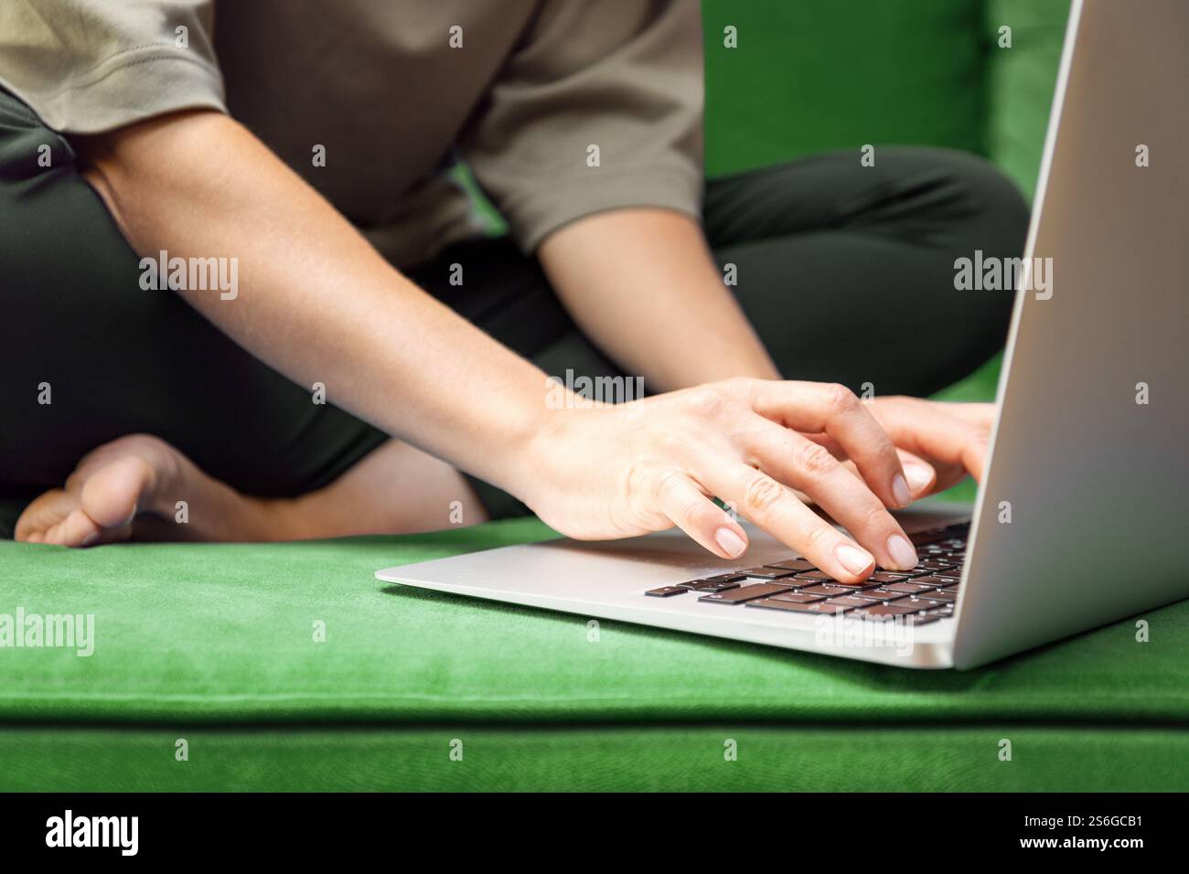 Woman sitting on green sofa and typing on laptop keyboard Stock Photo ...