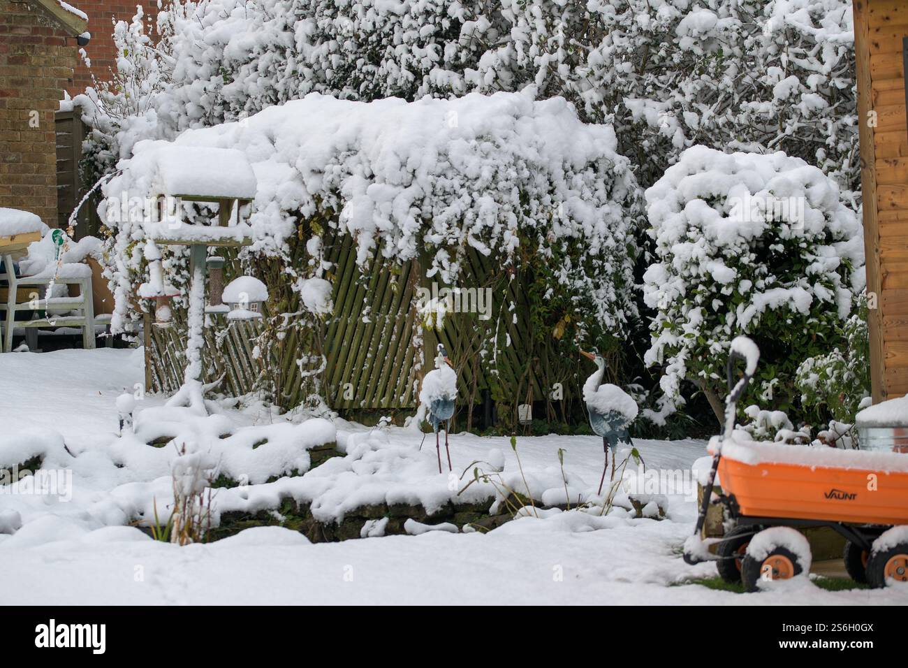 Snow-Covered Backyard Scene with Trees, Birdhouse, and Orange trolley and snow covered metal ...