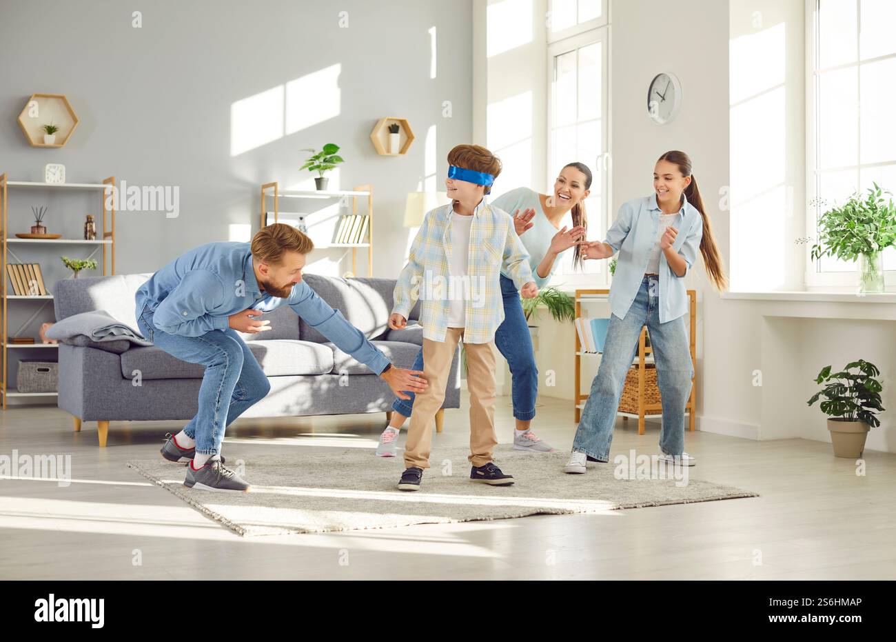 Happy funny family at home, mother and father with two children playing blind man's buff game ...