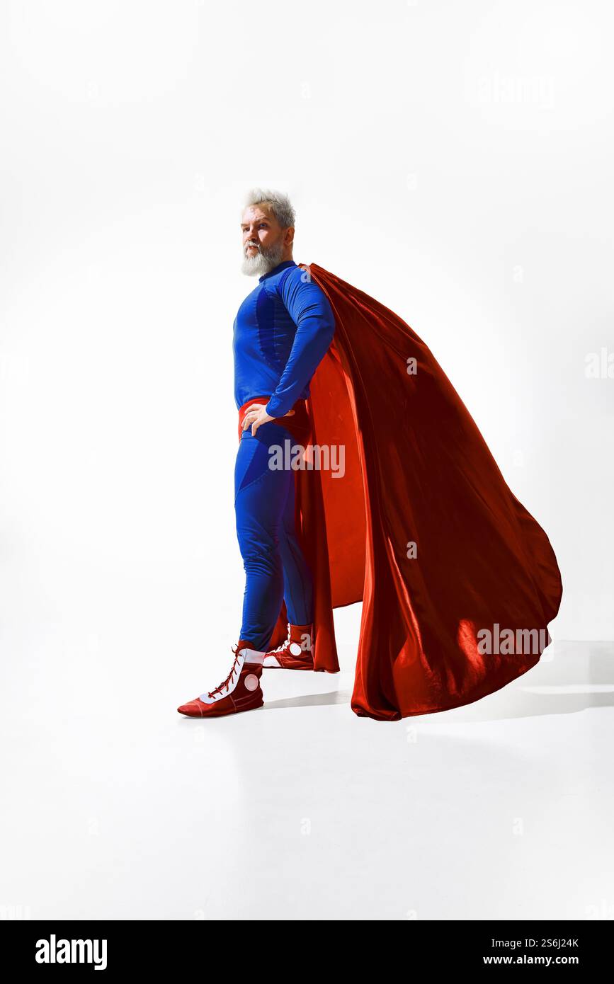 Gray-haired man in blue superhero outfit and red cape stands tall and ...