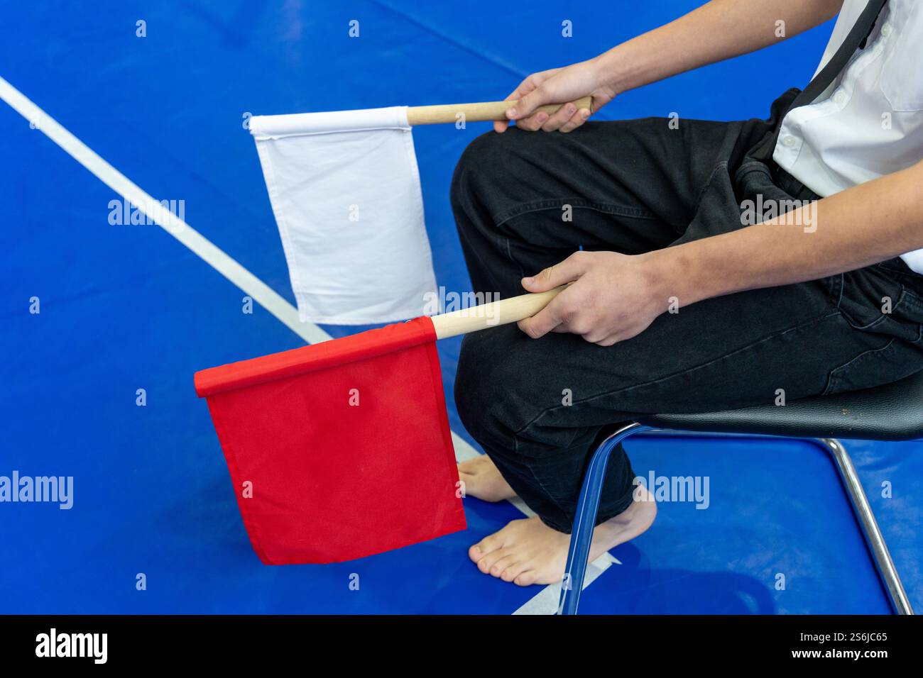 The karate referee sitting beside the mat with red and white flags in ...