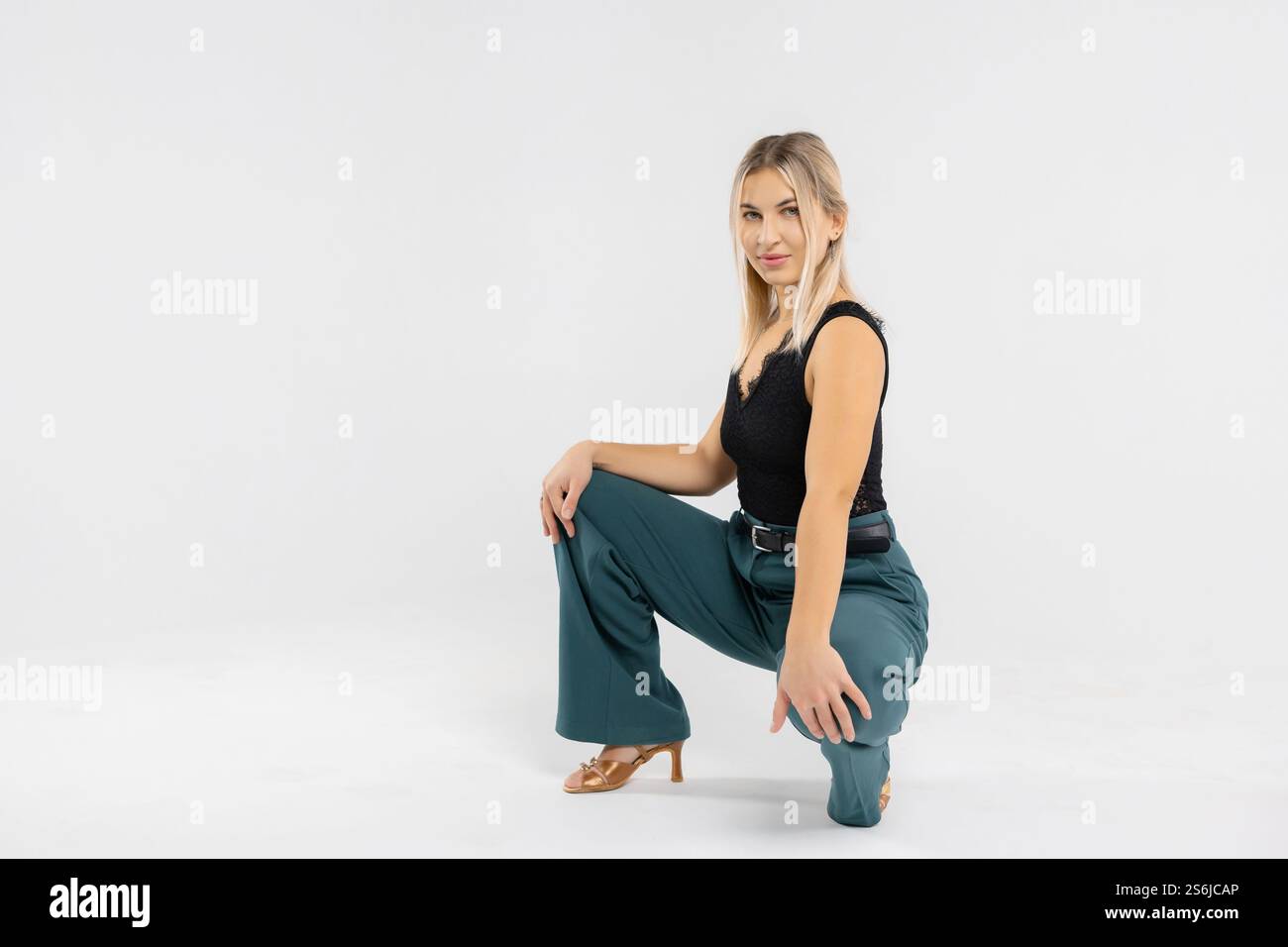 Young blonde woman in elegant office wear, crouching in a studio ...