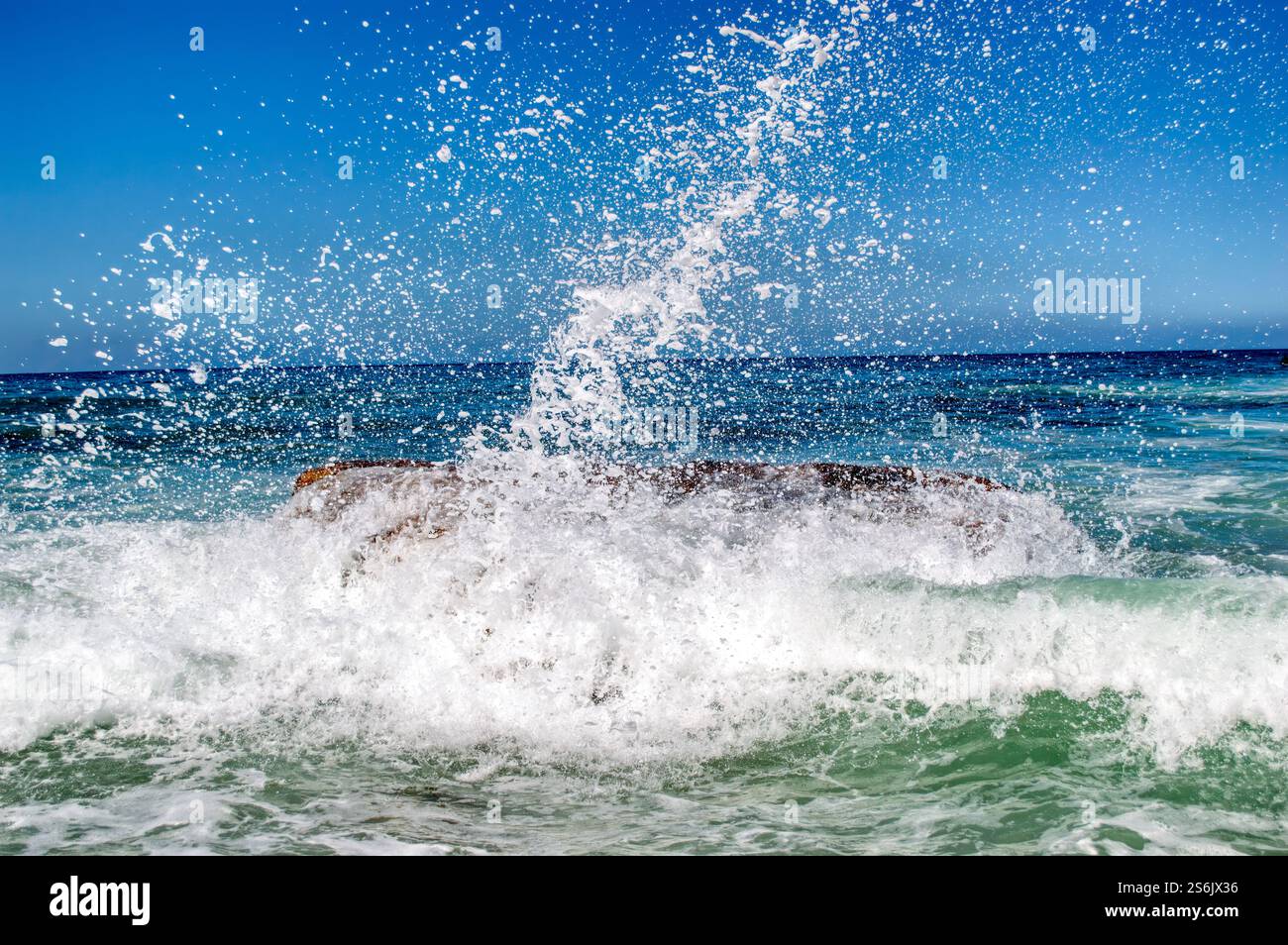 wave splashing on a giant stone in the ocean, spray bubbles in the blue ...