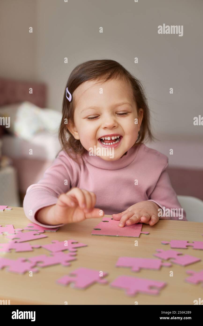 Cute little child girl connecting puzzle pieces on wooden desk in room ...