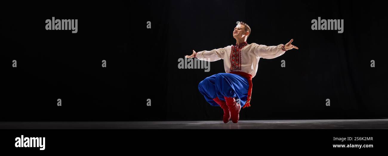 Male dancer in embroidered shirt and red boots leaping gracefully, arms ...