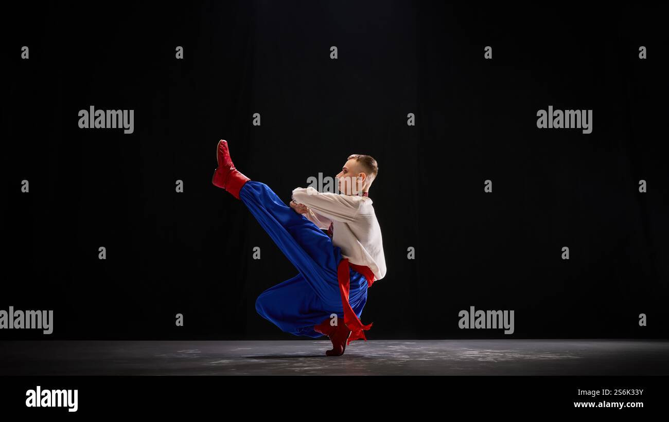 Performer in low squatting pose, one leg extended, hands crossed on ...