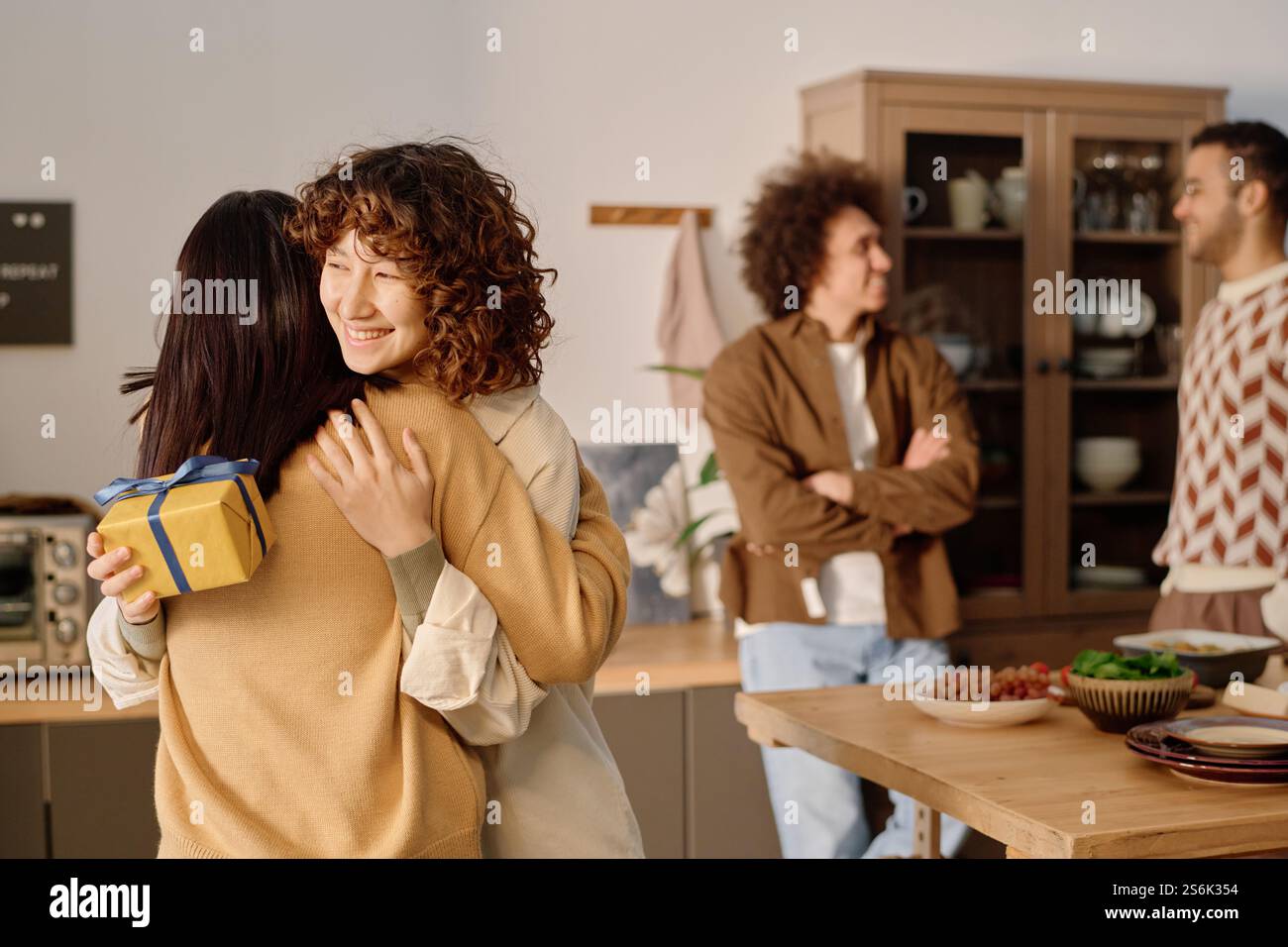 Medium close up of smiling woman holding gift box while hugging her ...