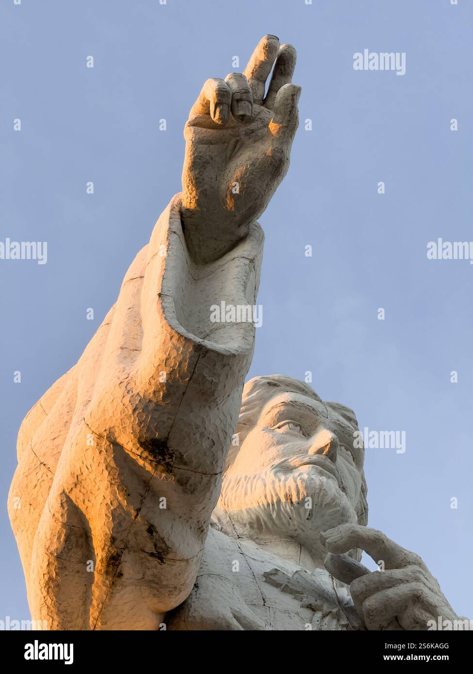 Towering statue of figure raising one hand, illuminated by warm sunset ...