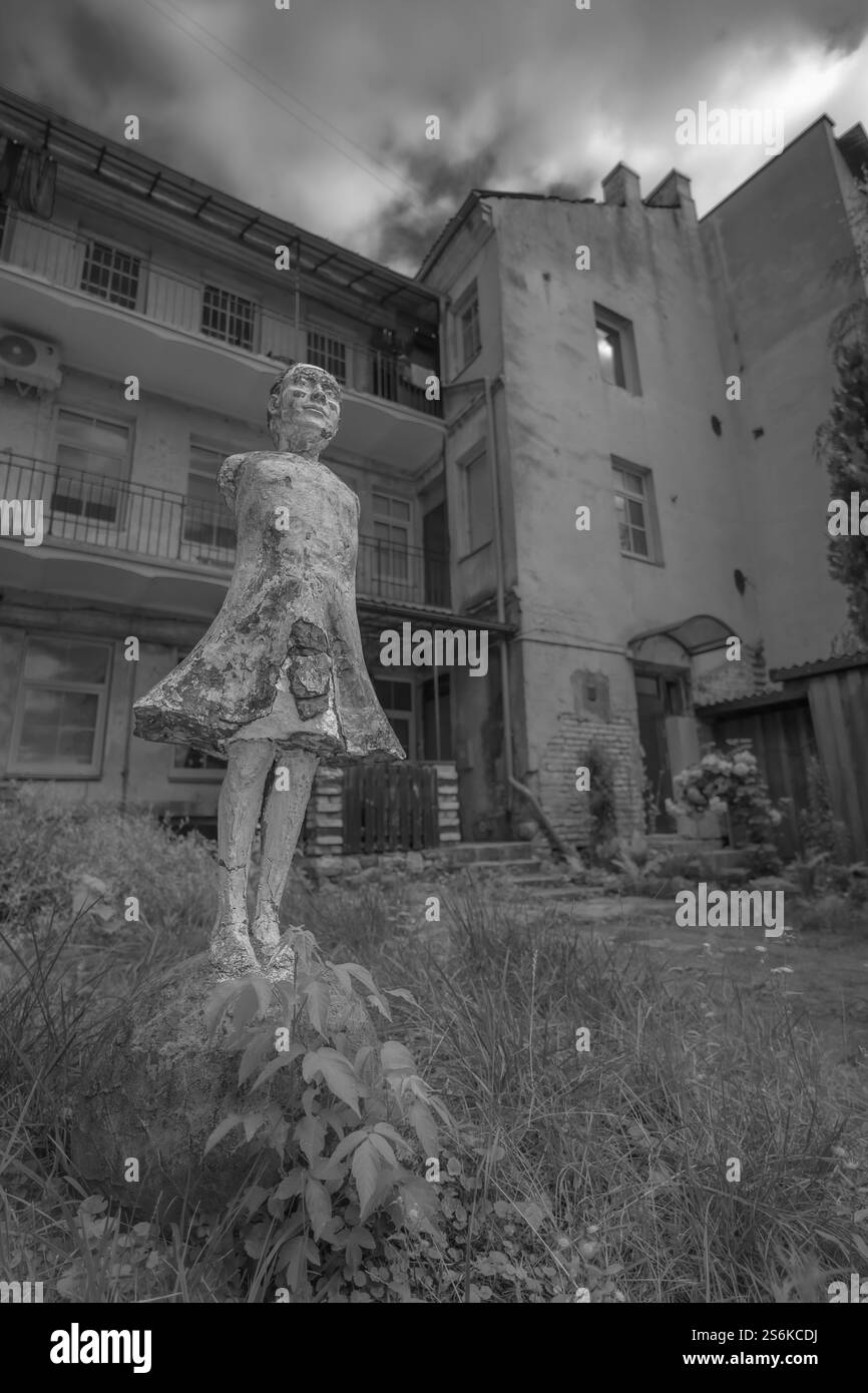 A weathered concrete statue of a figure in a dilapidated courtyard. The ...