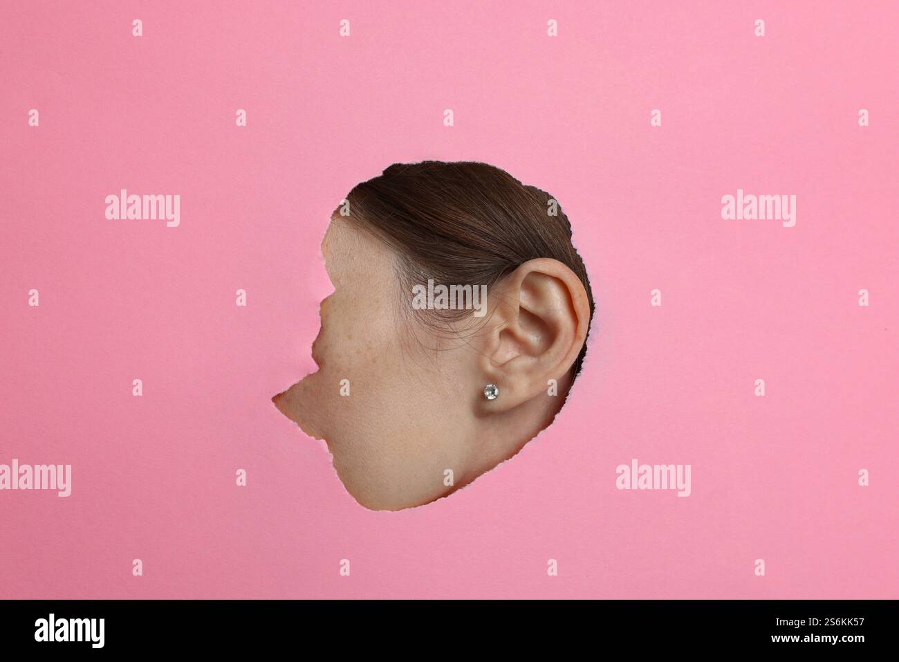 Woman showing her ear through hole in pink paper, closeup Stock Photo ...
