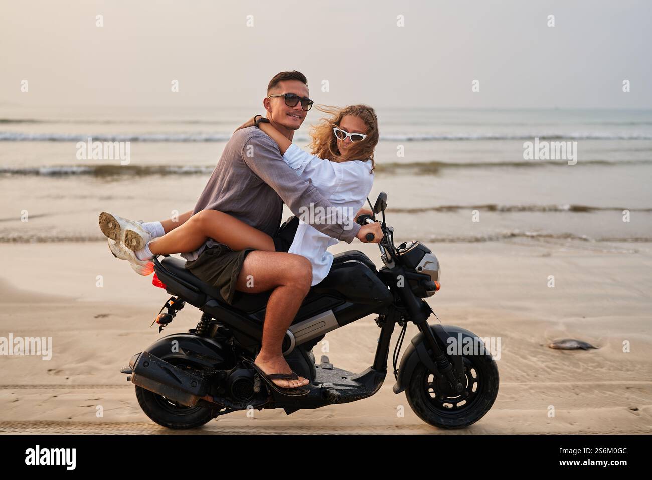 Couple rides motorcycle on beach. Man drives motorbike, woman hugs him ...