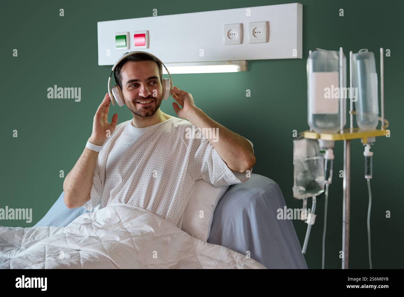 Male patient sitting in bed in hospital ward, wearing headphones and ...