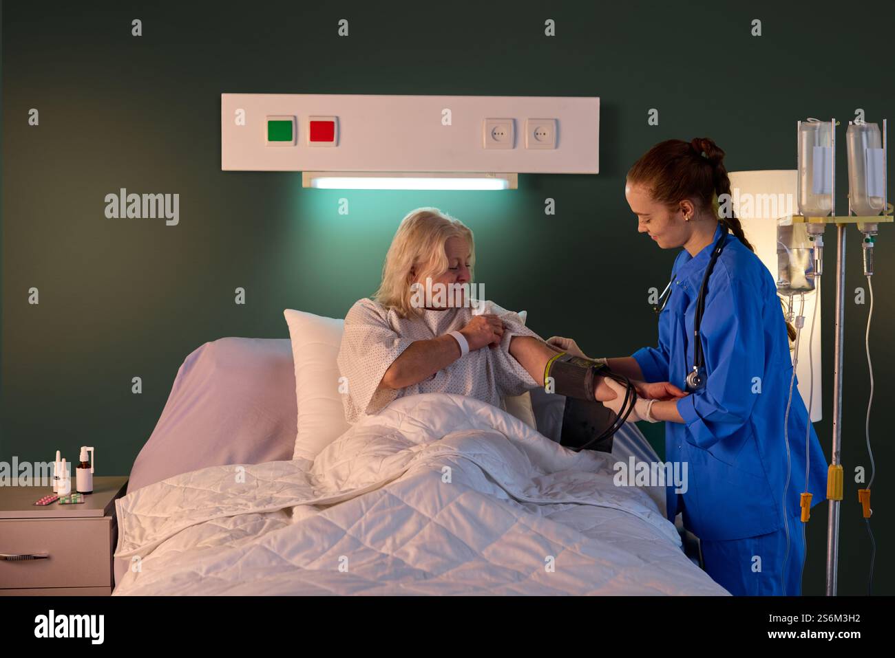 Elderly woman lying in hospital bed, young nurse measuring her blood ...