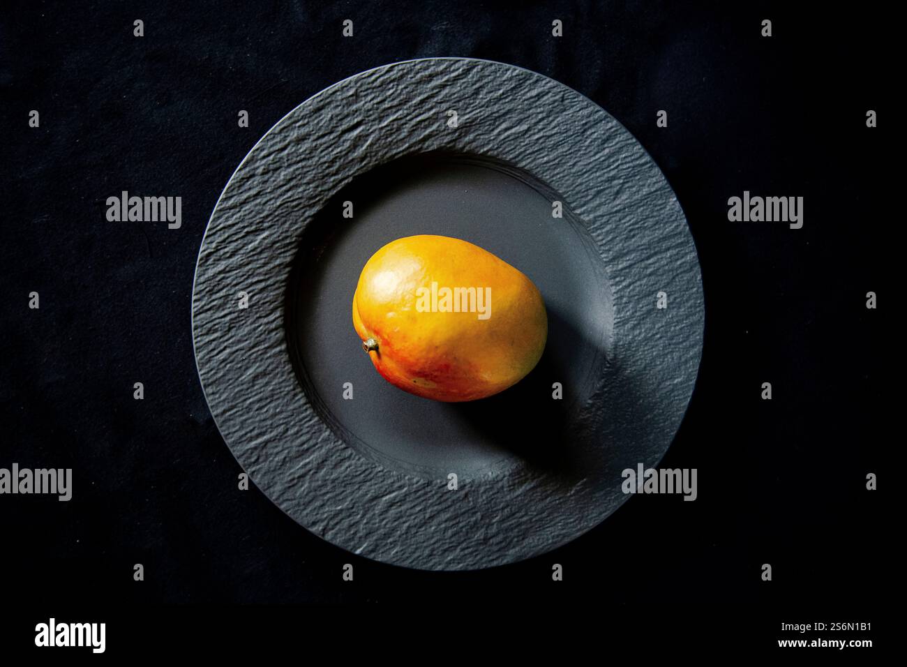 A golden-yellow mango on a black plate - free-standing Stock Photo - Alamy