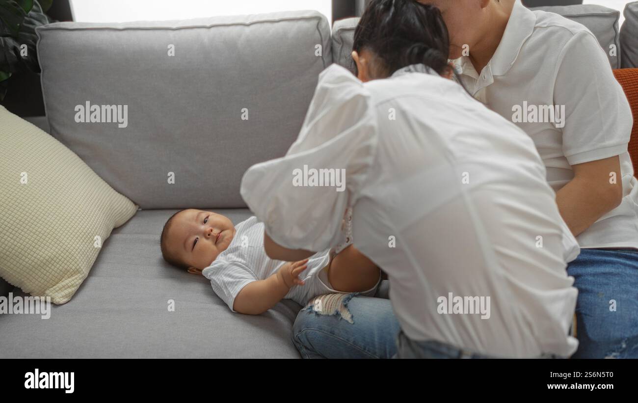 Mother changing baby diaper while father watches on sofa in cozy living ...