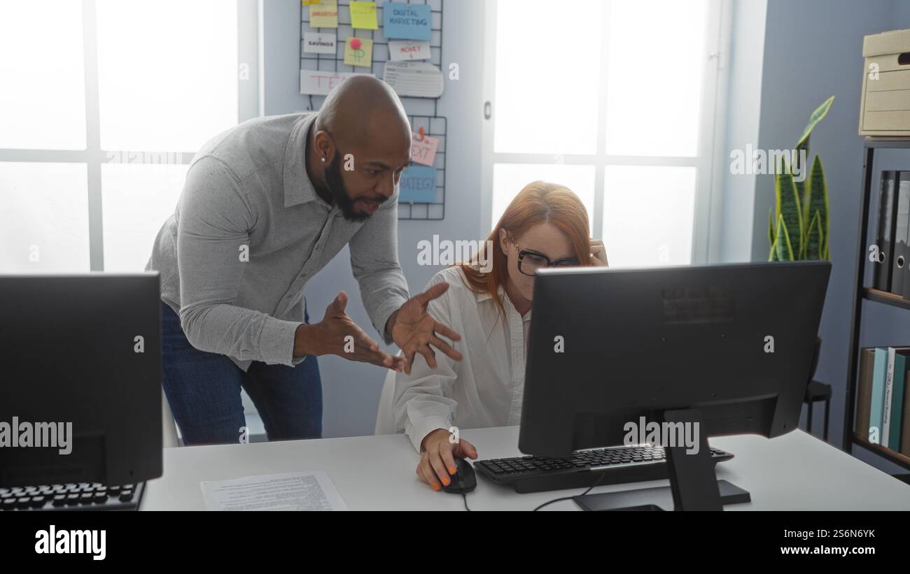 Man explaining work to woman in office, both focused on computer screen ...
